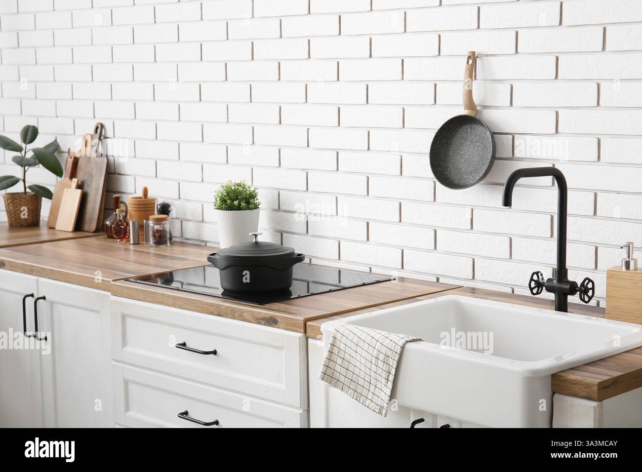 Kitchen counters with stove, utensils and sink near white brick wall ...