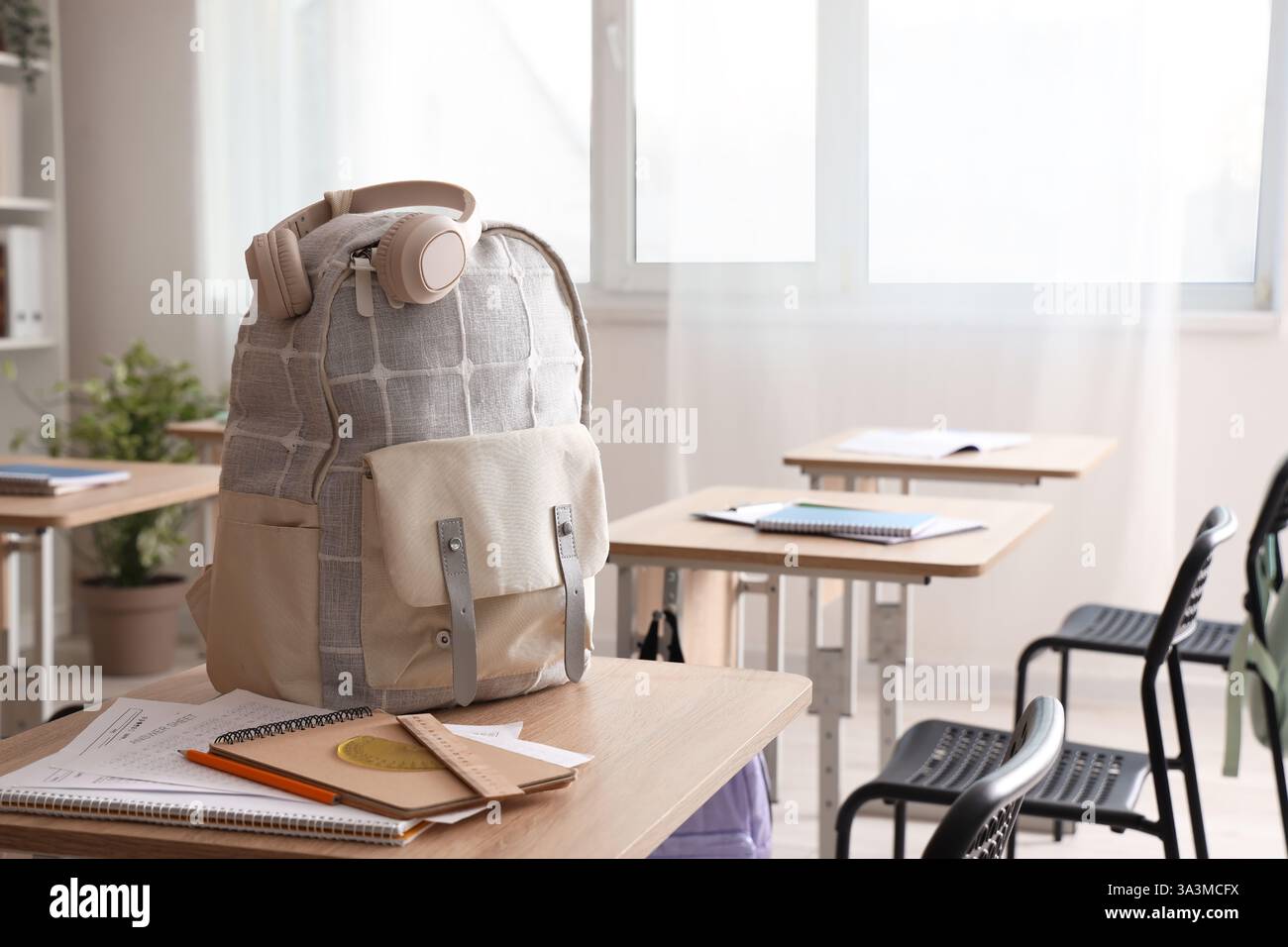 Backpack with headphones and school stationery on desk in classroom ...