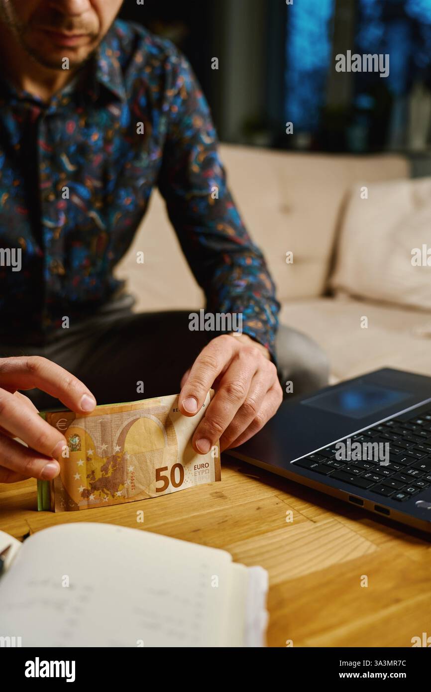 Man holding euro banknotes, sitting on sofa in front of table with ...