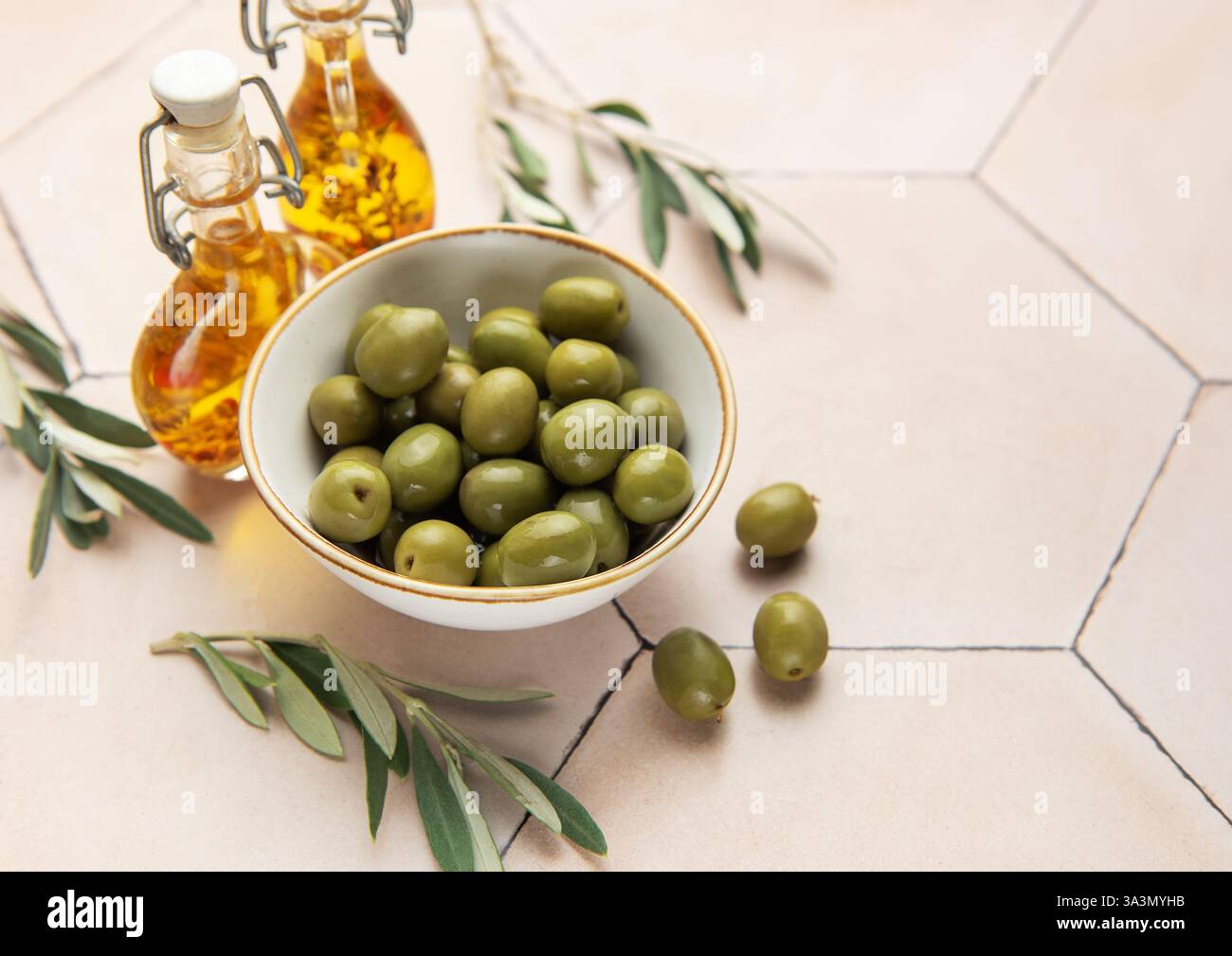 Green table olives with olive oil bottles and olive tree branches ...