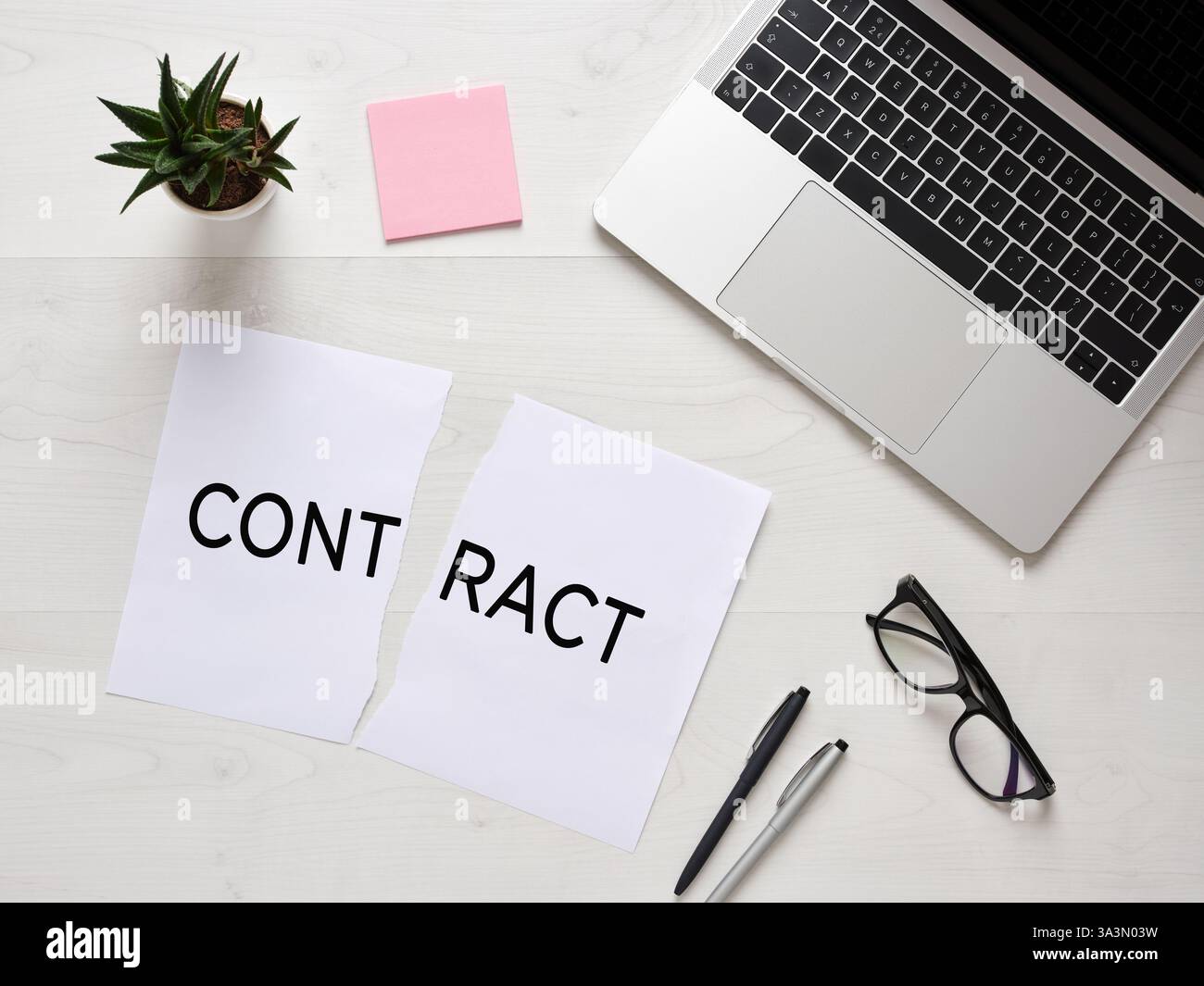 Torn contract on white wooden desk with laptop, pens, glasses, plant ...