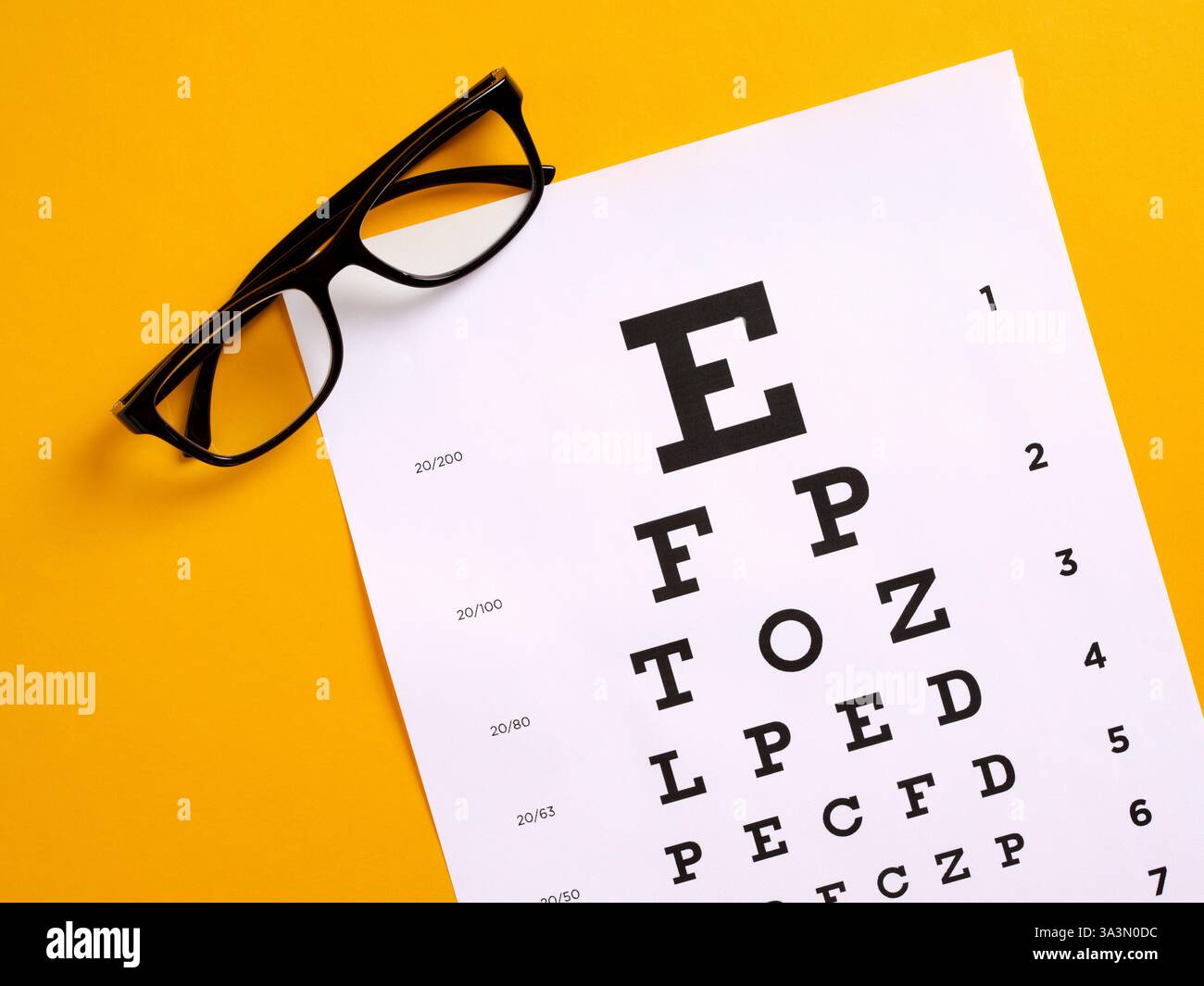 Eye exam chart and glasses lying on a yellow background, representing ...