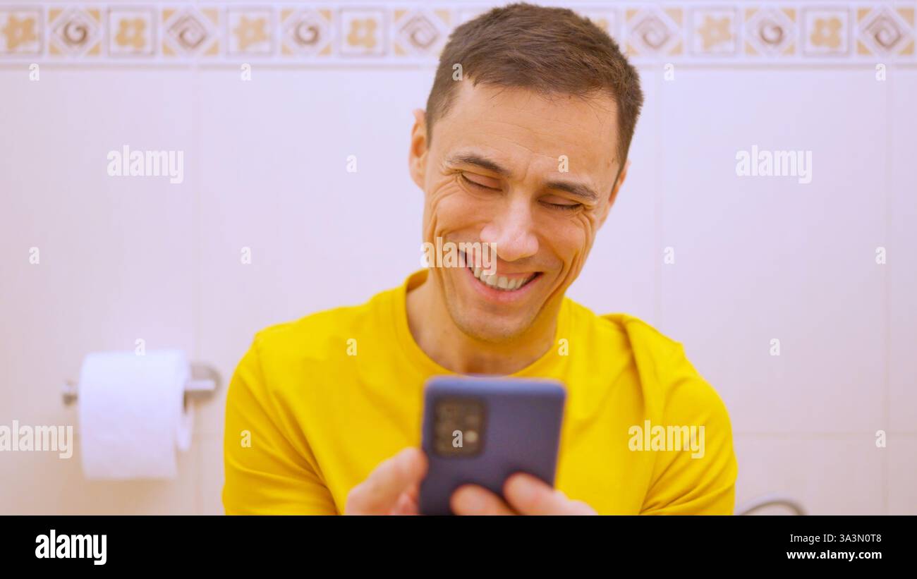 Man laughing while using smartphone on toilet in bathroom Stock Photo ...