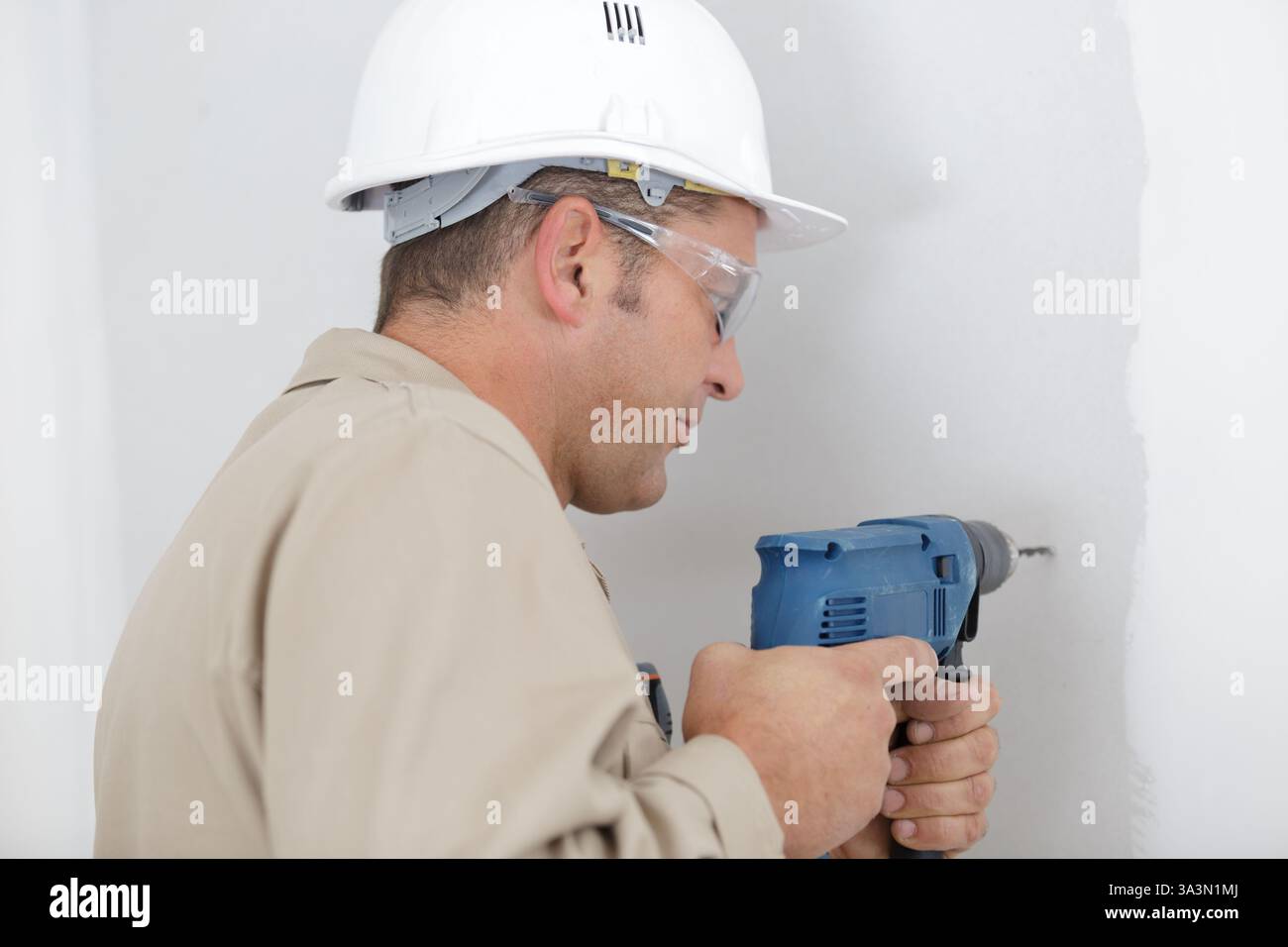 mature tradesman using drill on interior wall Stock Photo - Alamy
