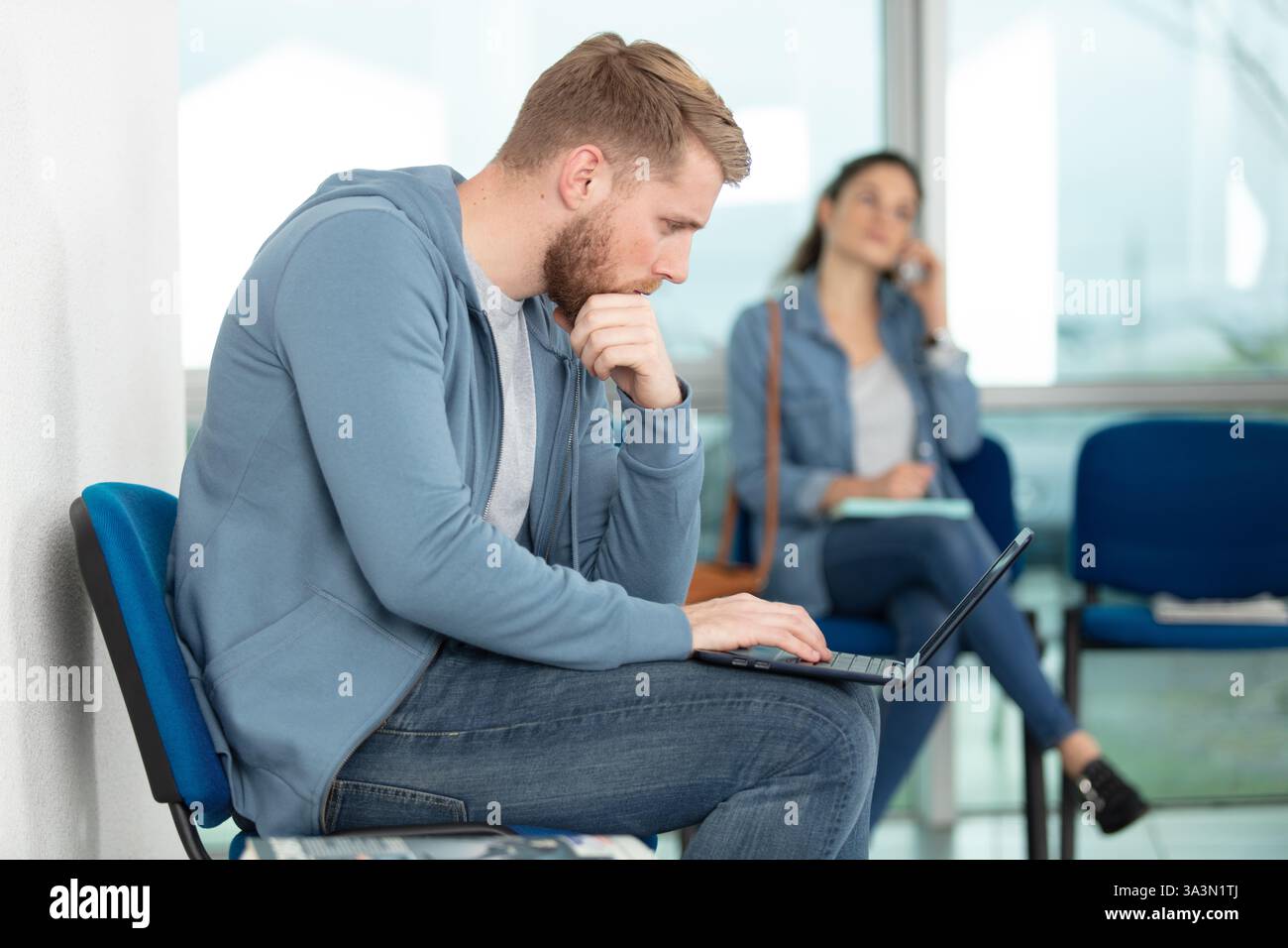 young man in waiting room using computer Stock Photo - Alamy