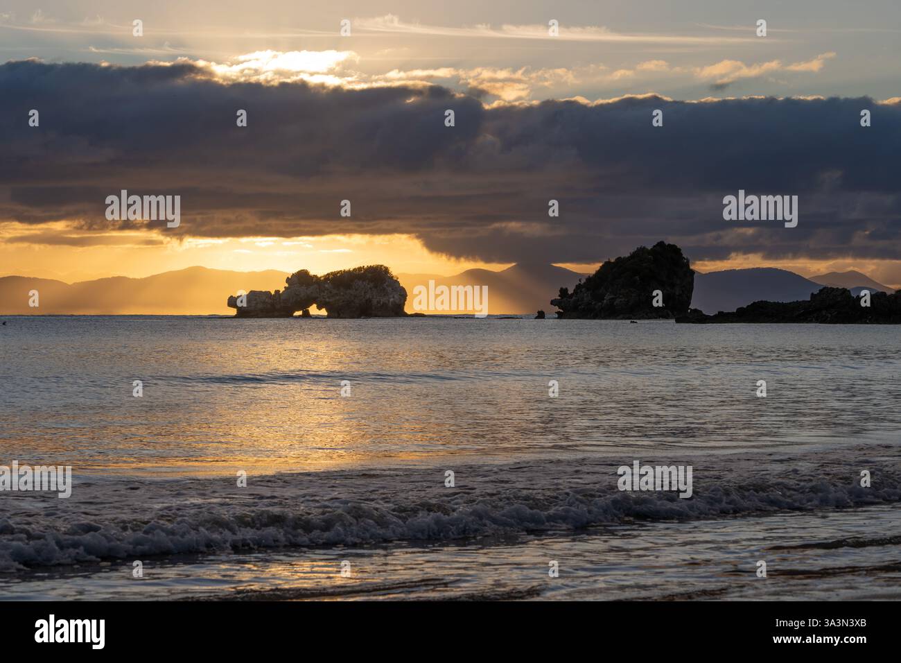 Sunrise through island cave with waves in foreground, distant hills of ...
