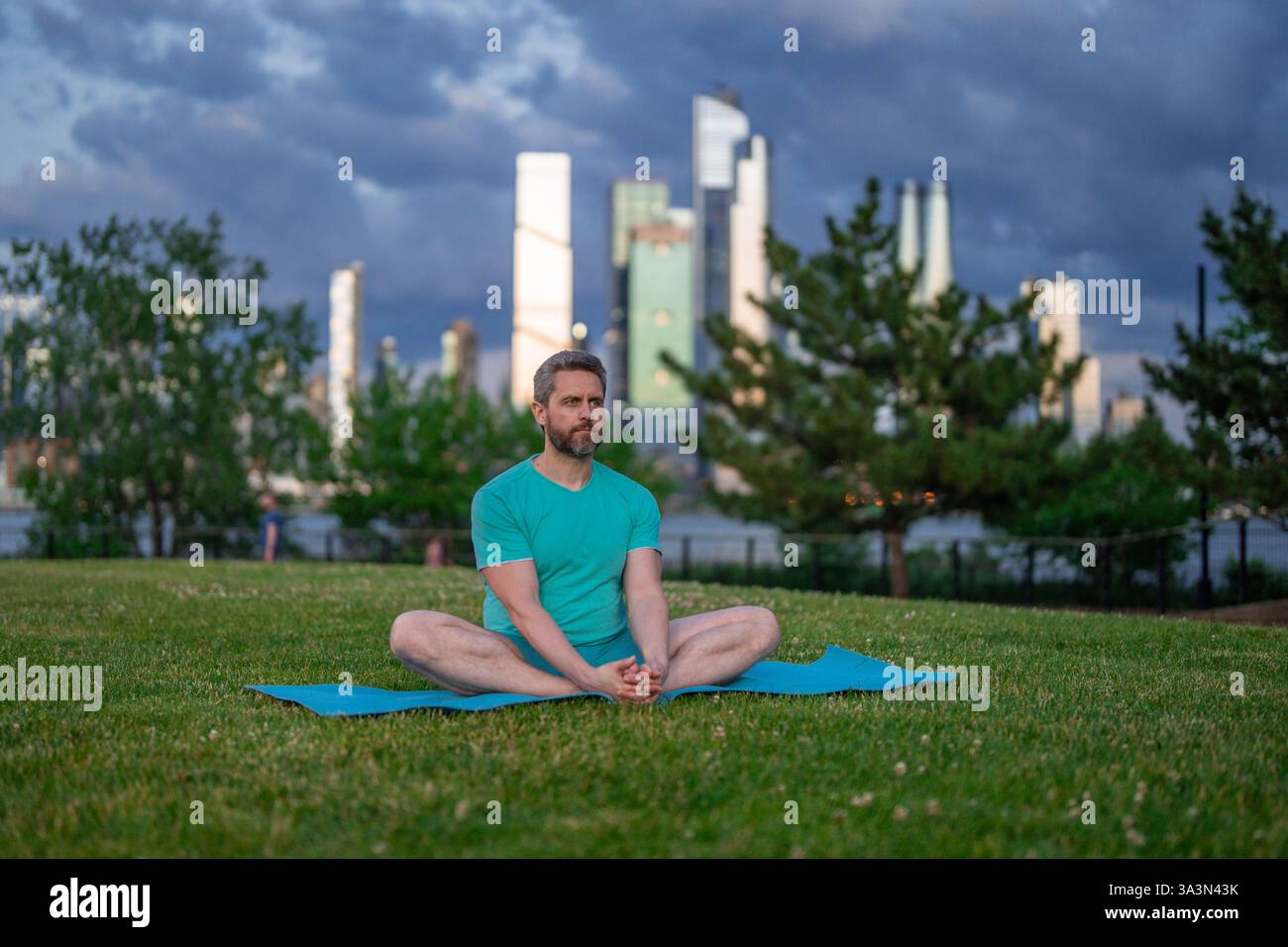 Mature Man meditating in lotus pose in grass outdoors. Sportsman doing ...