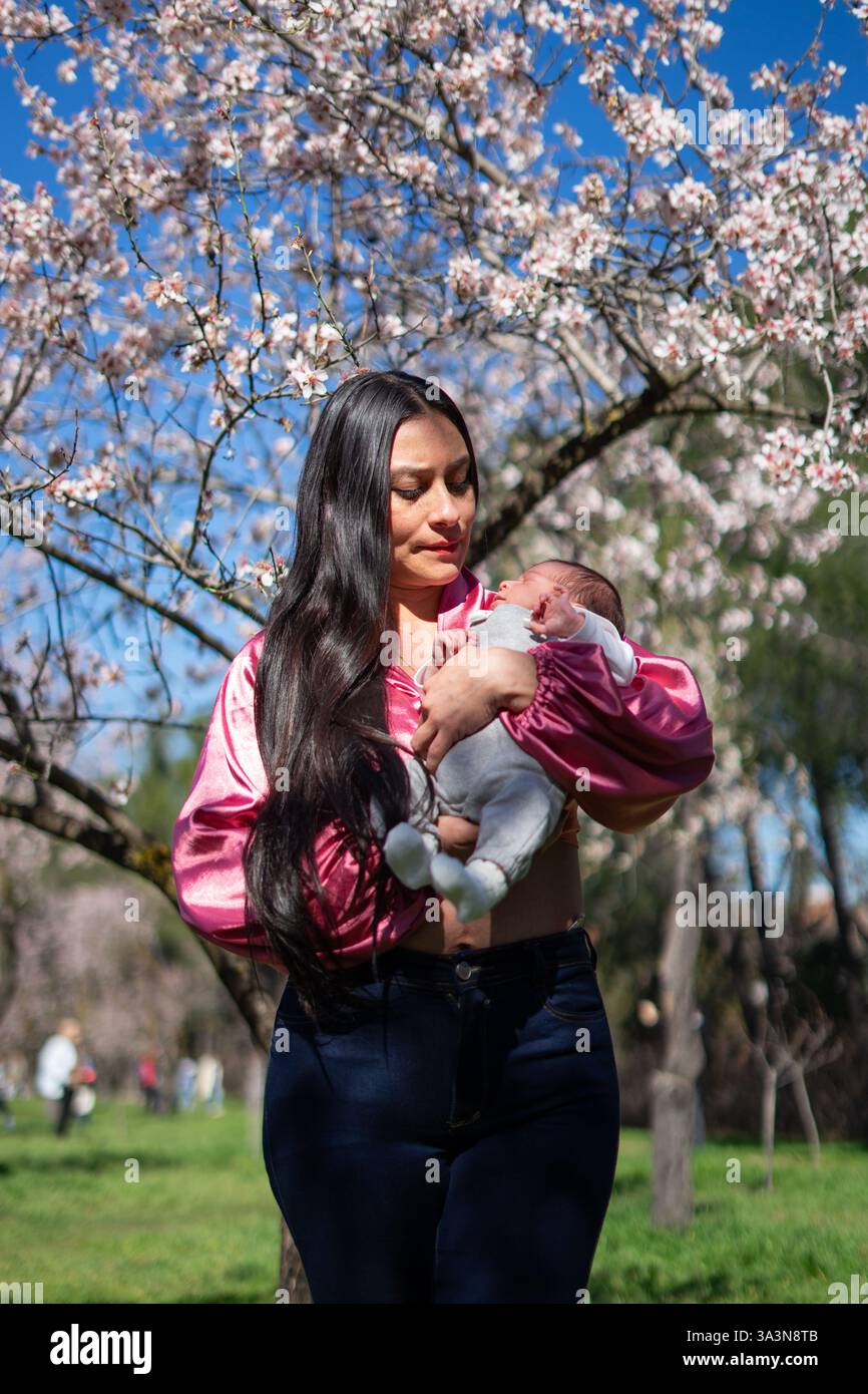 Latin mother holding her newborn baby under an almond tree in full ...