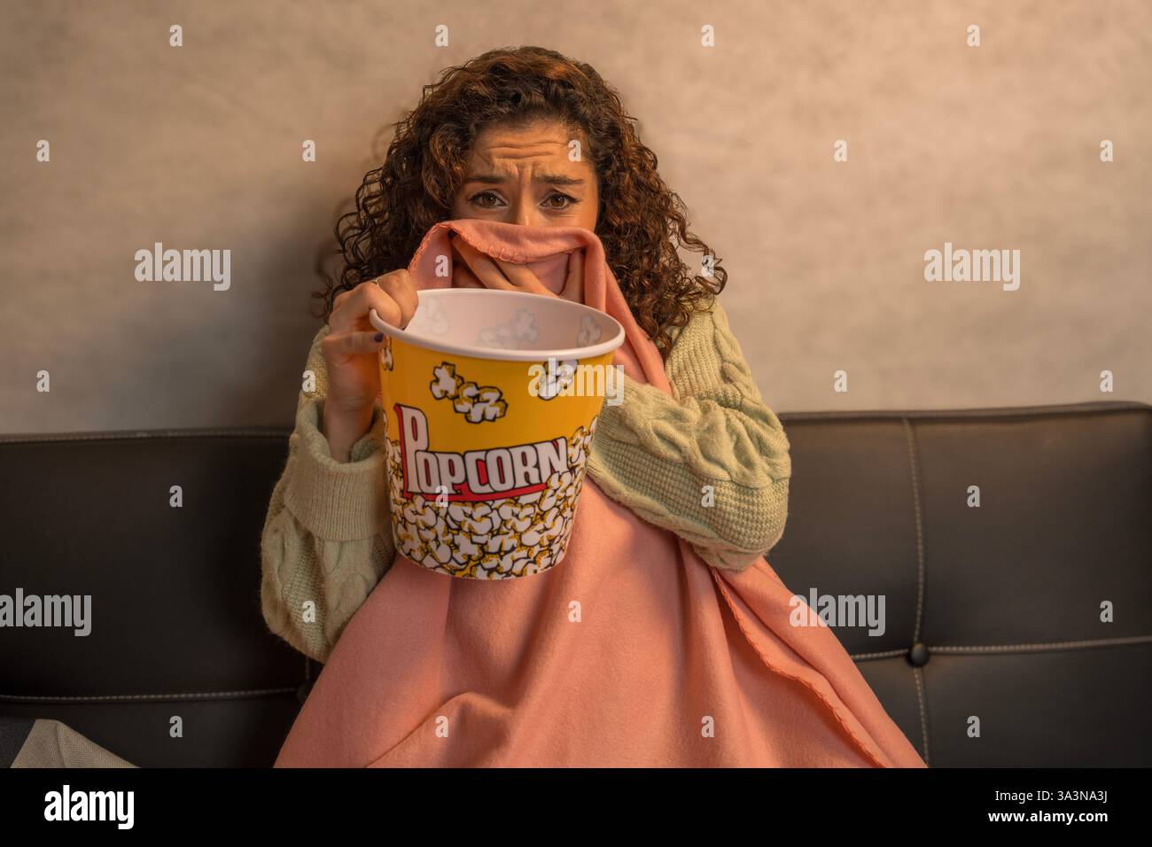 Frightened woman watching a horror movie on tv hiding behind a blanket ...