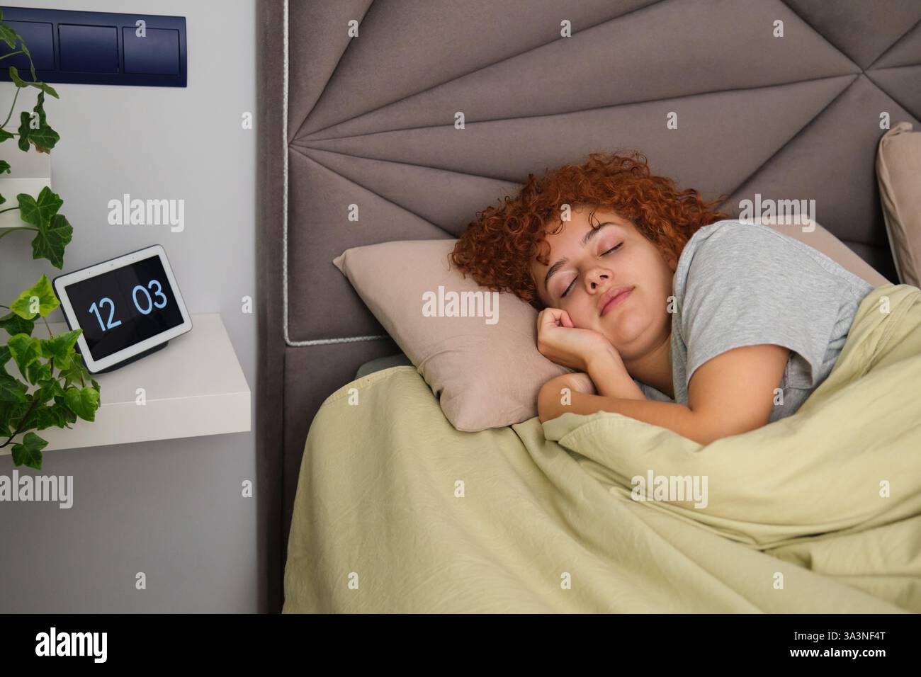 Young woman sleeping peacefully in bed, digital clock showing midday ...
