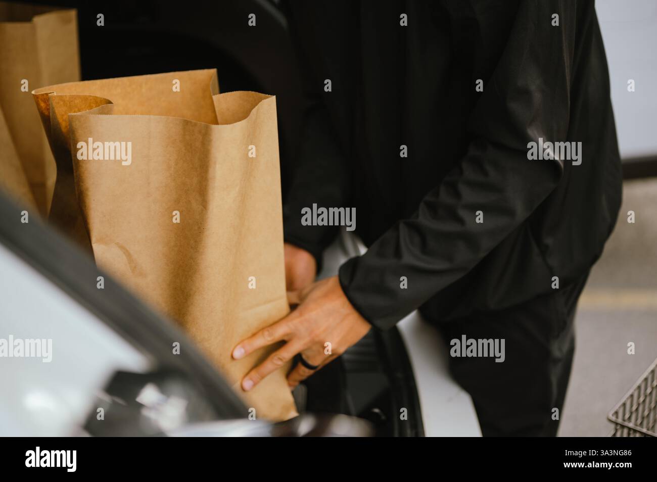 Midsection of young man placing paper grocery bags into trunk of car ...