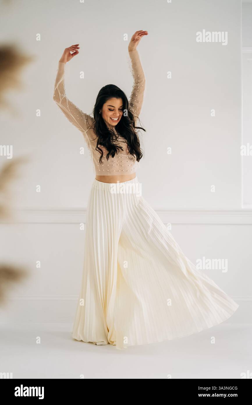 Woman twirling joyfully in pleated skirt and sheer top, arms raised ...