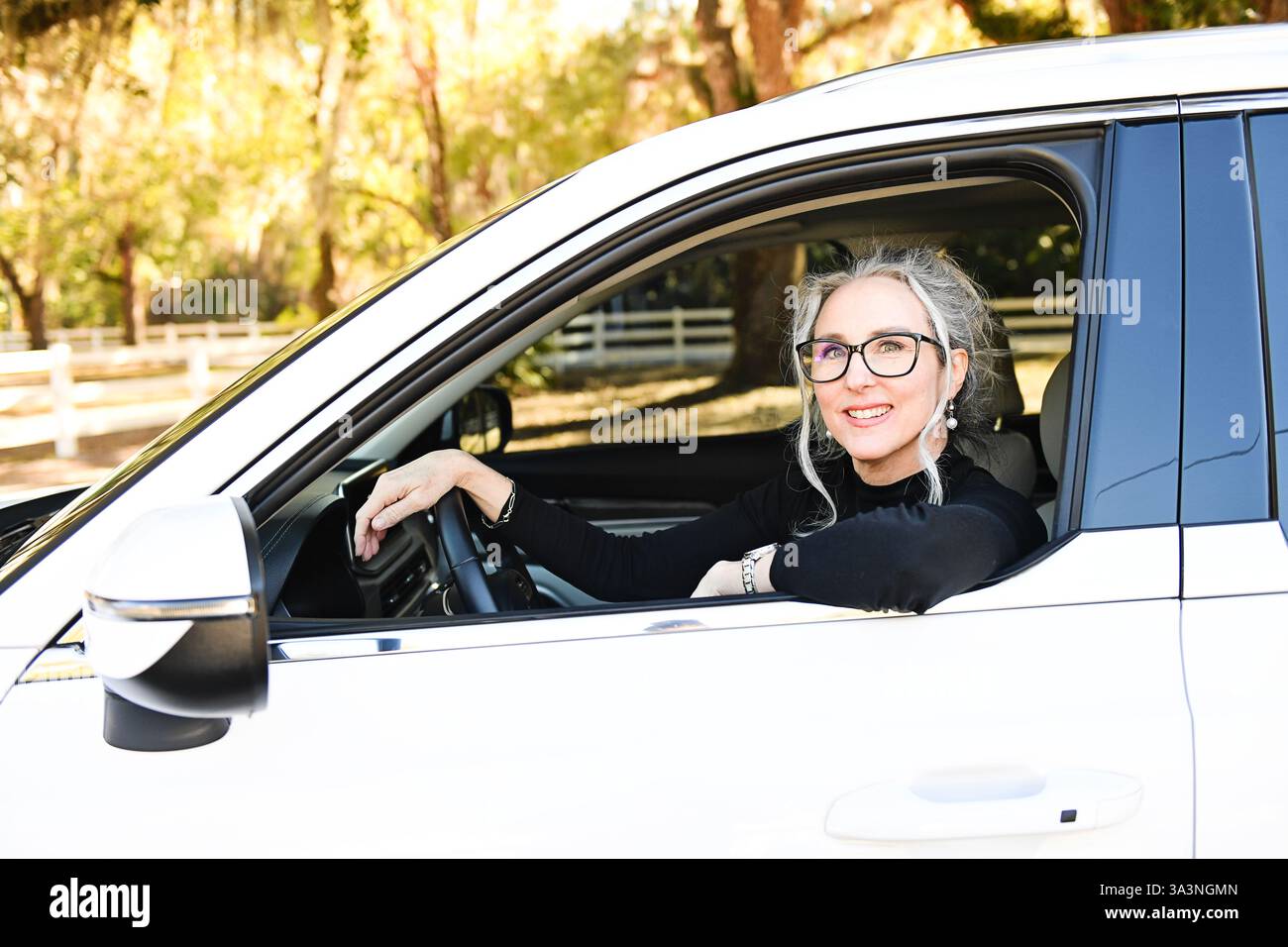 Woman smiling through the open window of a white SUV, arm restin Stock ...