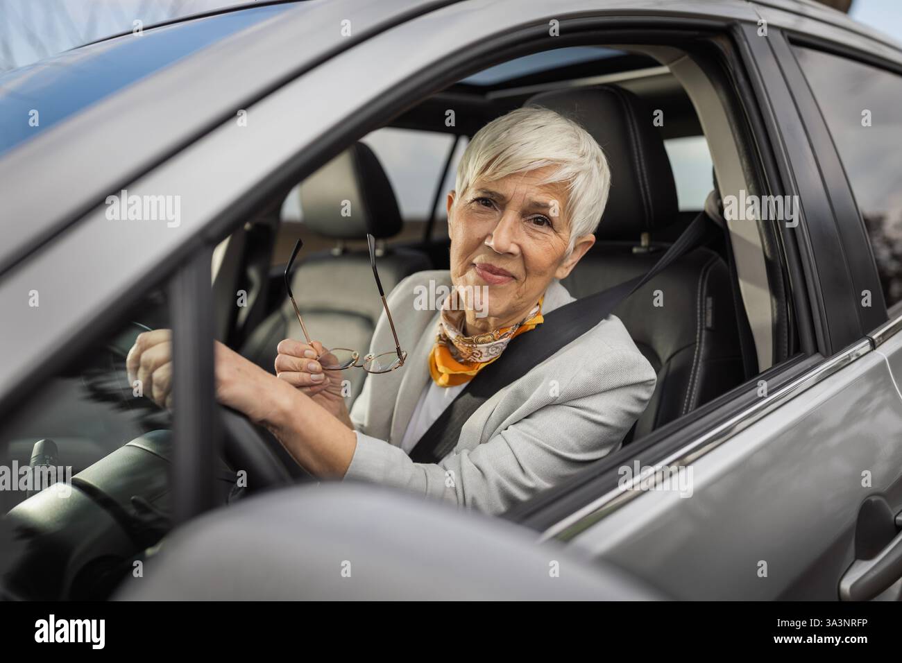 Senior woman with short silver hair smiles while holding her glasses in ...
