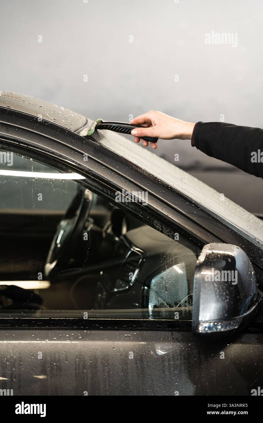 Removing water from windscreen using scraper at car wash service ...