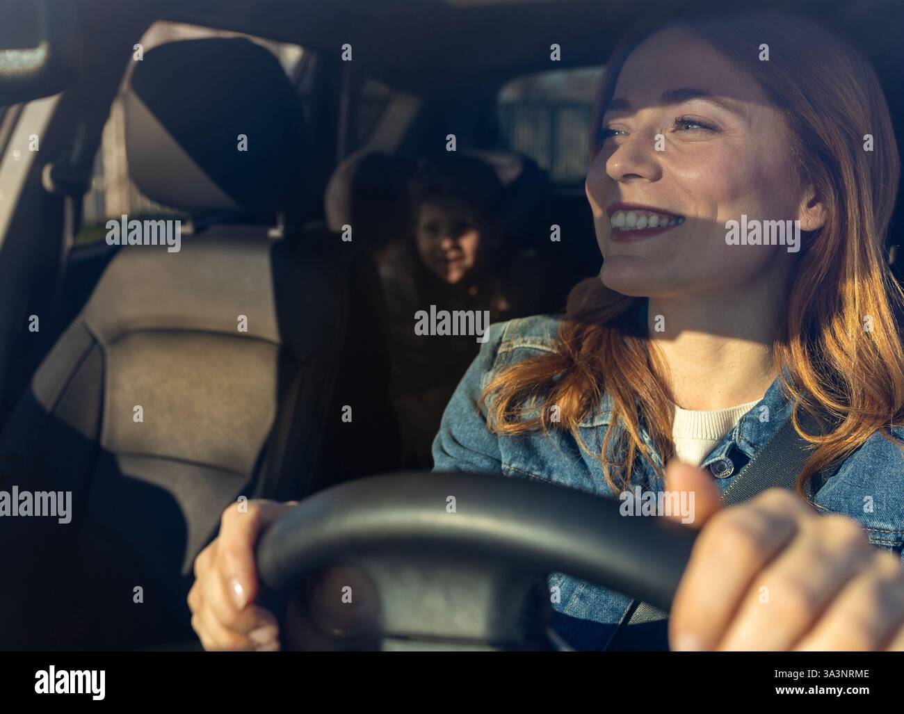 Woman smiling while driving car, with child seated comfortably in ...