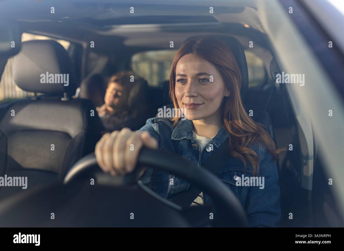 Woman smiling while driving car, with child seated comfortably in ...