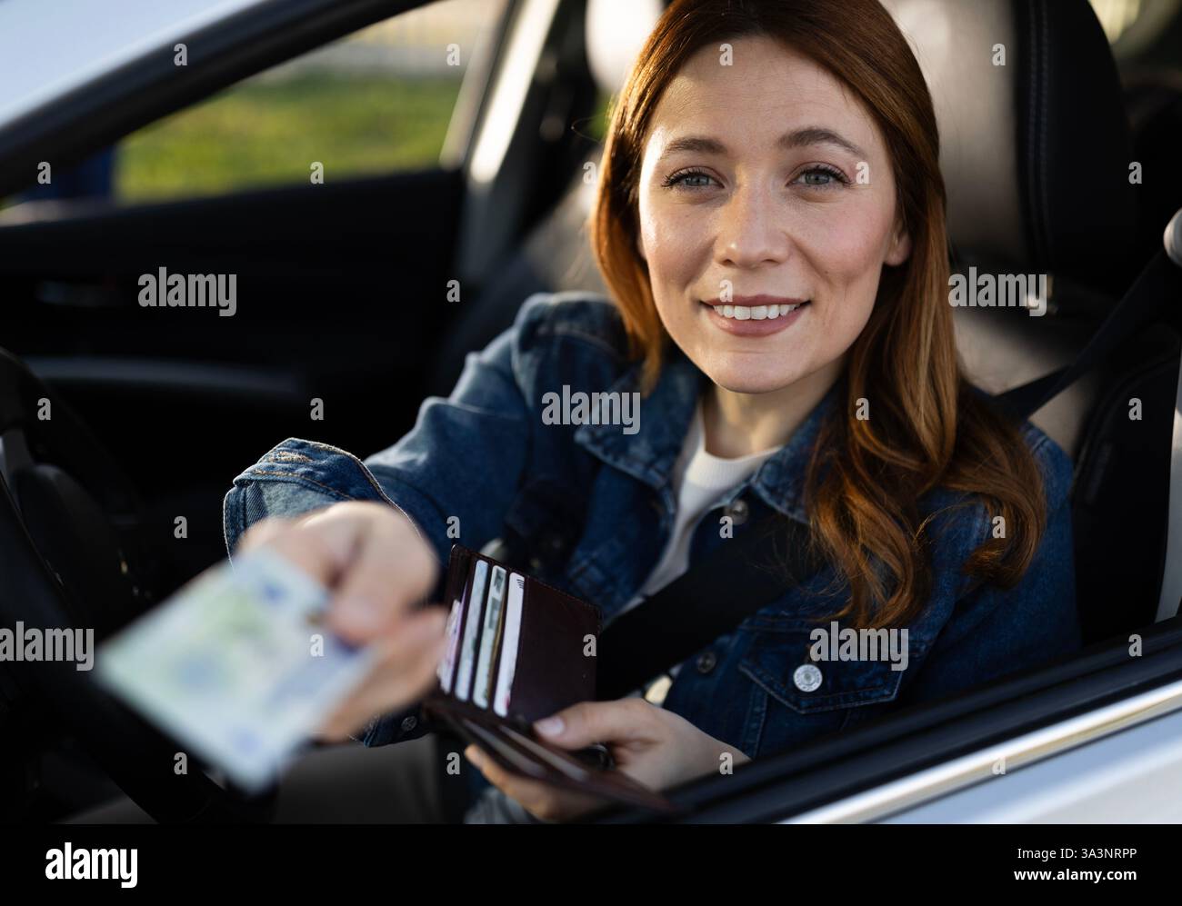 Young pretty woman seated on driver's seat in car giving ID card or driver licence to officer on ...