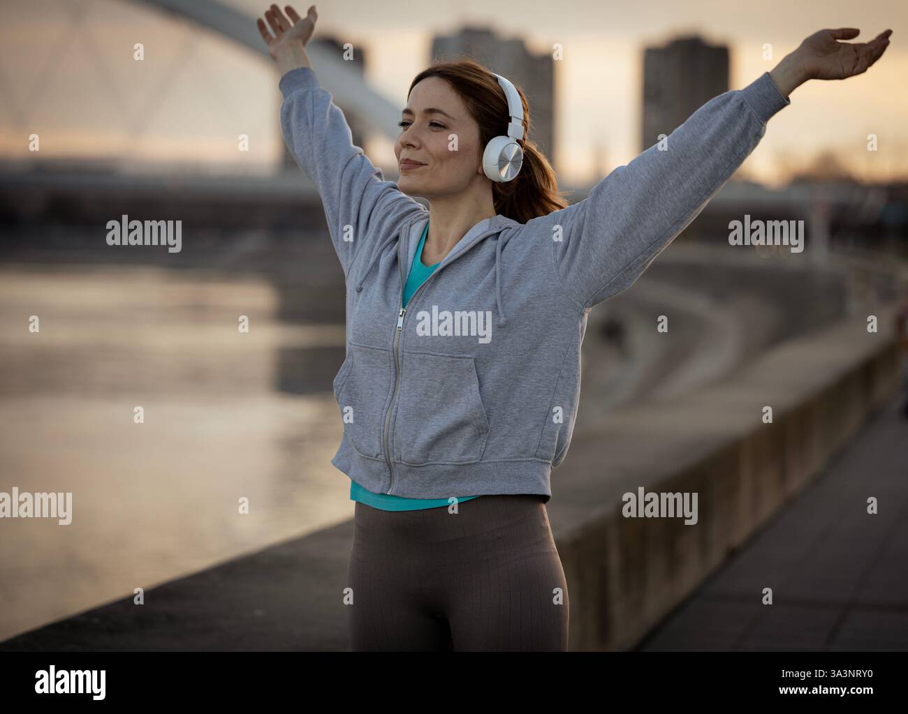 Pretty woman stretches with arms wide open by the riverside and ...