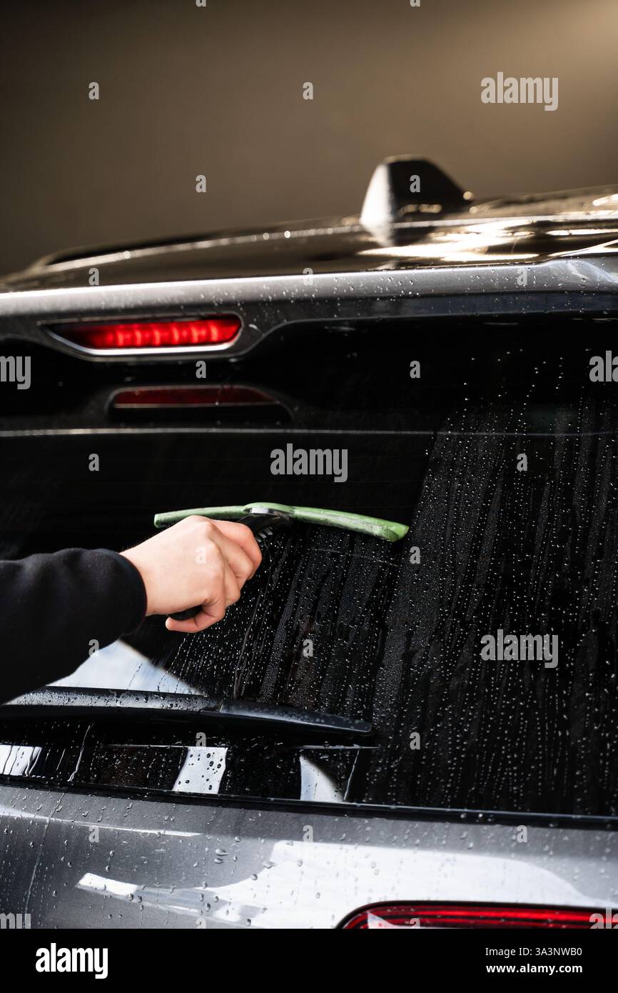 Removing water from glass surface of car using squeegee. Cleaning rear ...