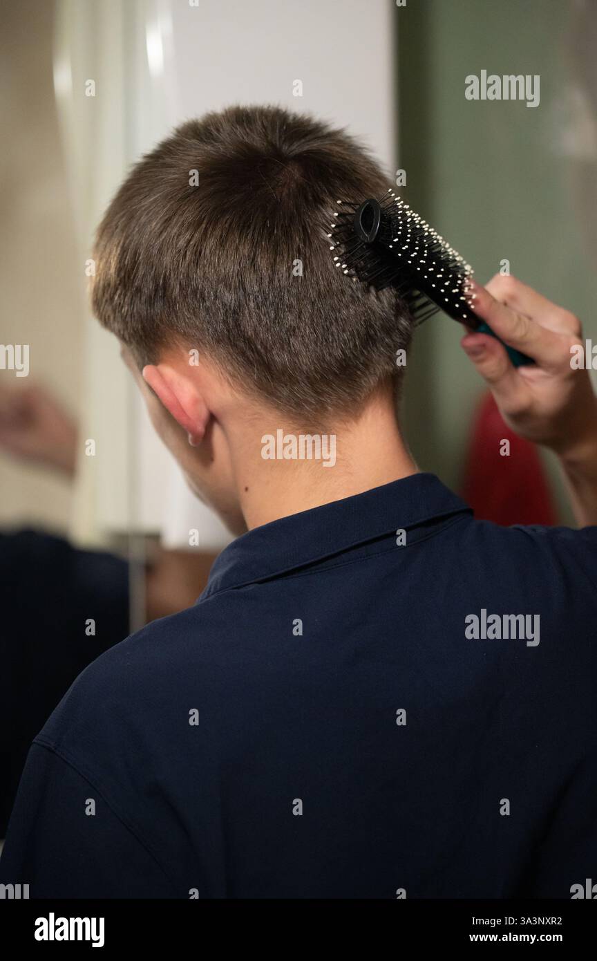 A young individual focuses on perfecting their hairstyle, using a round ...