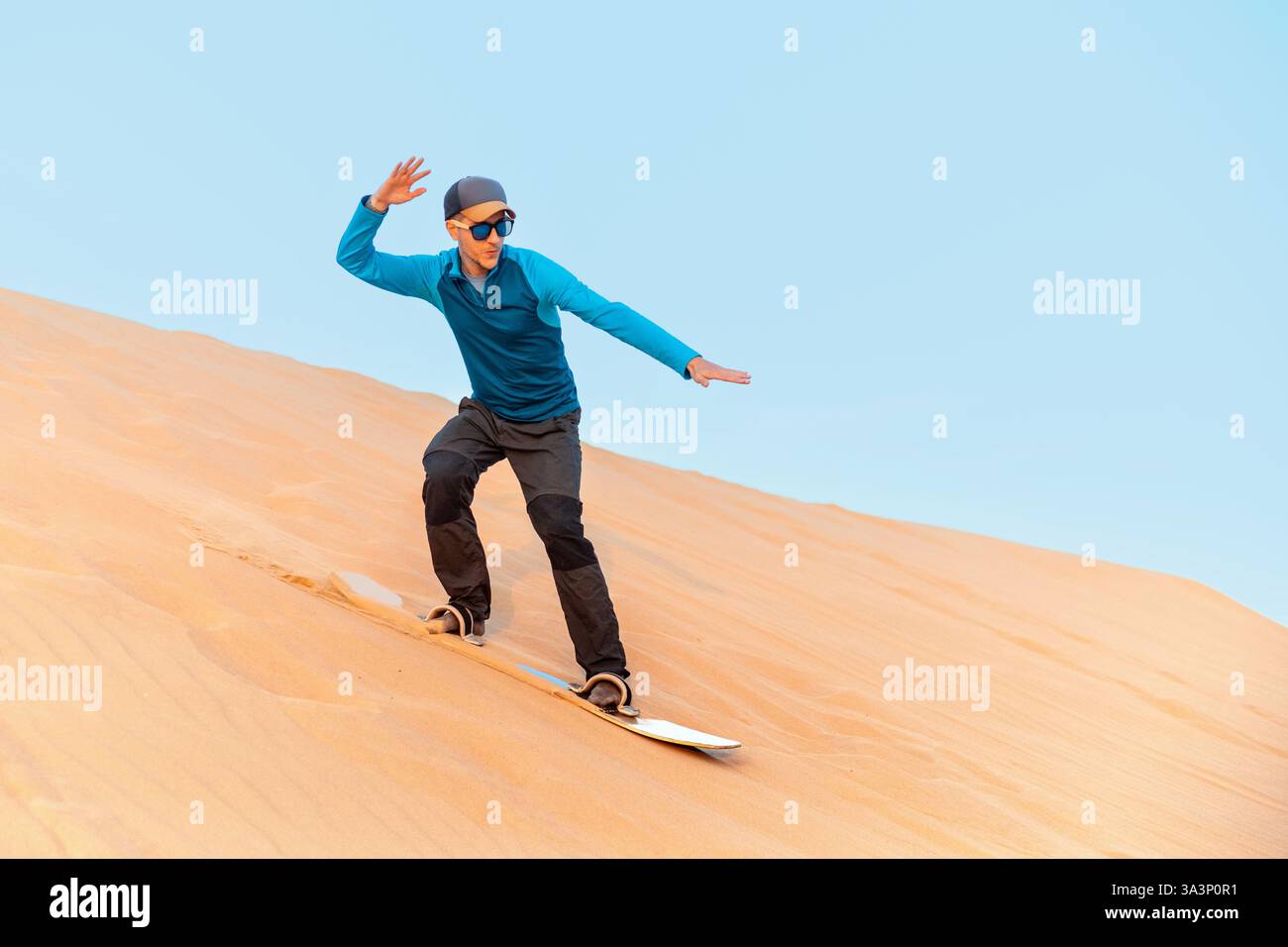 Tourist sandboarding down a steep dune in the desert, enjoying the ...