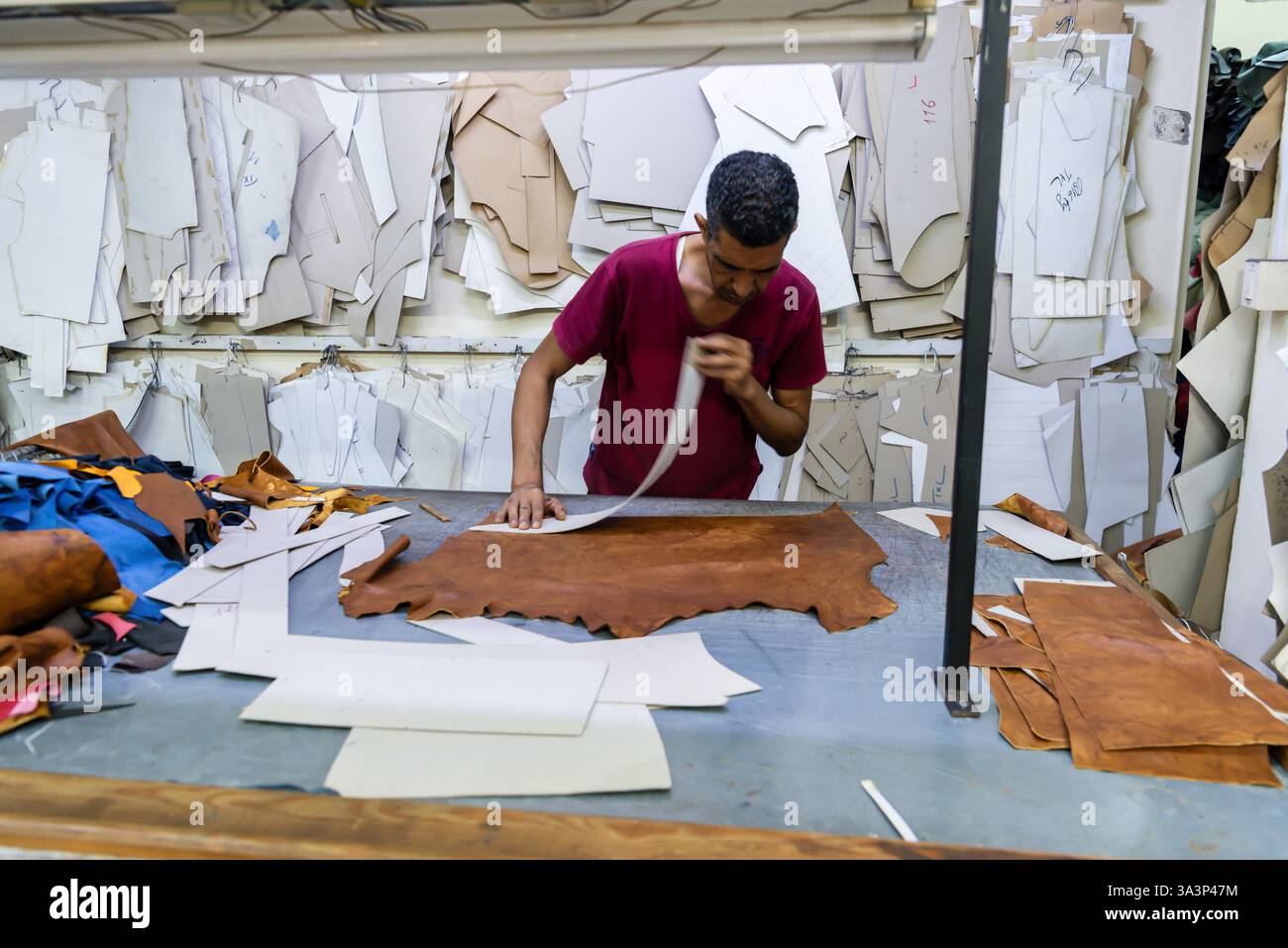A man uses a template to cut out leather in a leather factory, Tunisia ...
