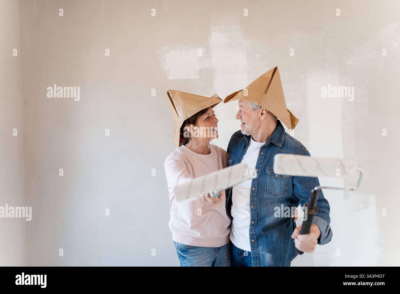 Portrait of cheerful senior couple painting walls with roller in new ...