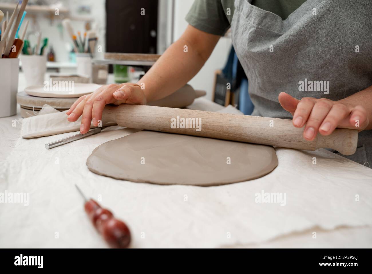 Rolling wooden stick to make flat sheet of clay. Preparing clay for ...
