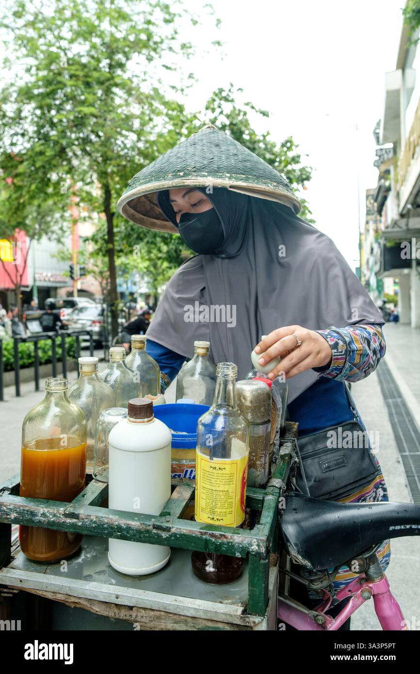 Street vendor wearing a mask and a traditional hat preparing herbal ...