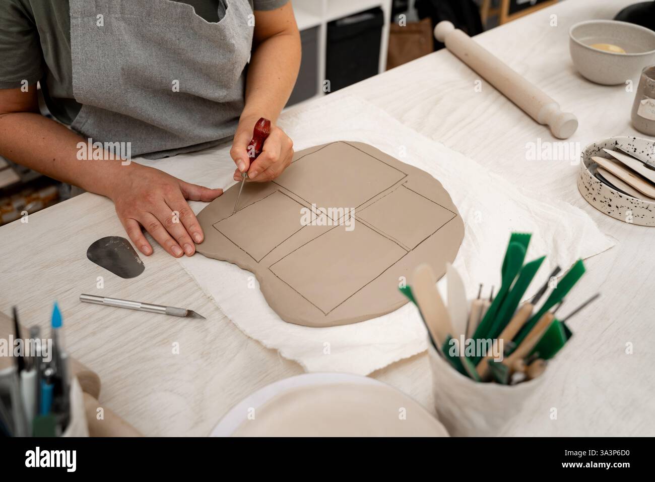 Using a sharp clay cutter to cut off a shape from the piece of clay ...