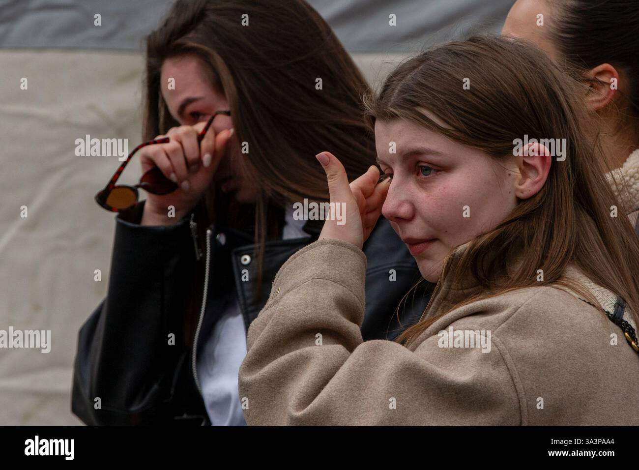 Women cry and wait in line to write condolence messages for the victims ...