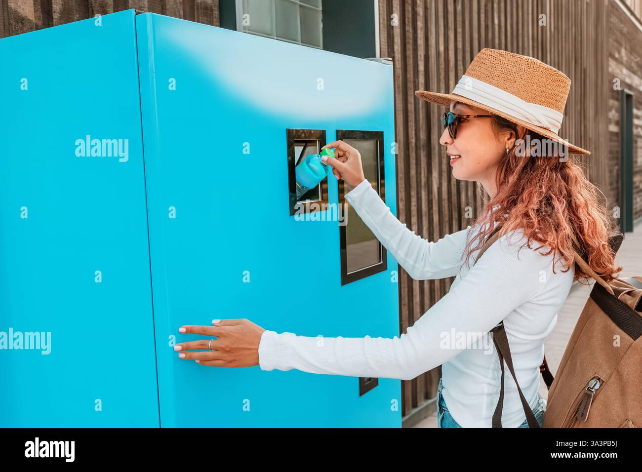 Tourist inserting a plastic bottle in a modern reverse vending machine ...