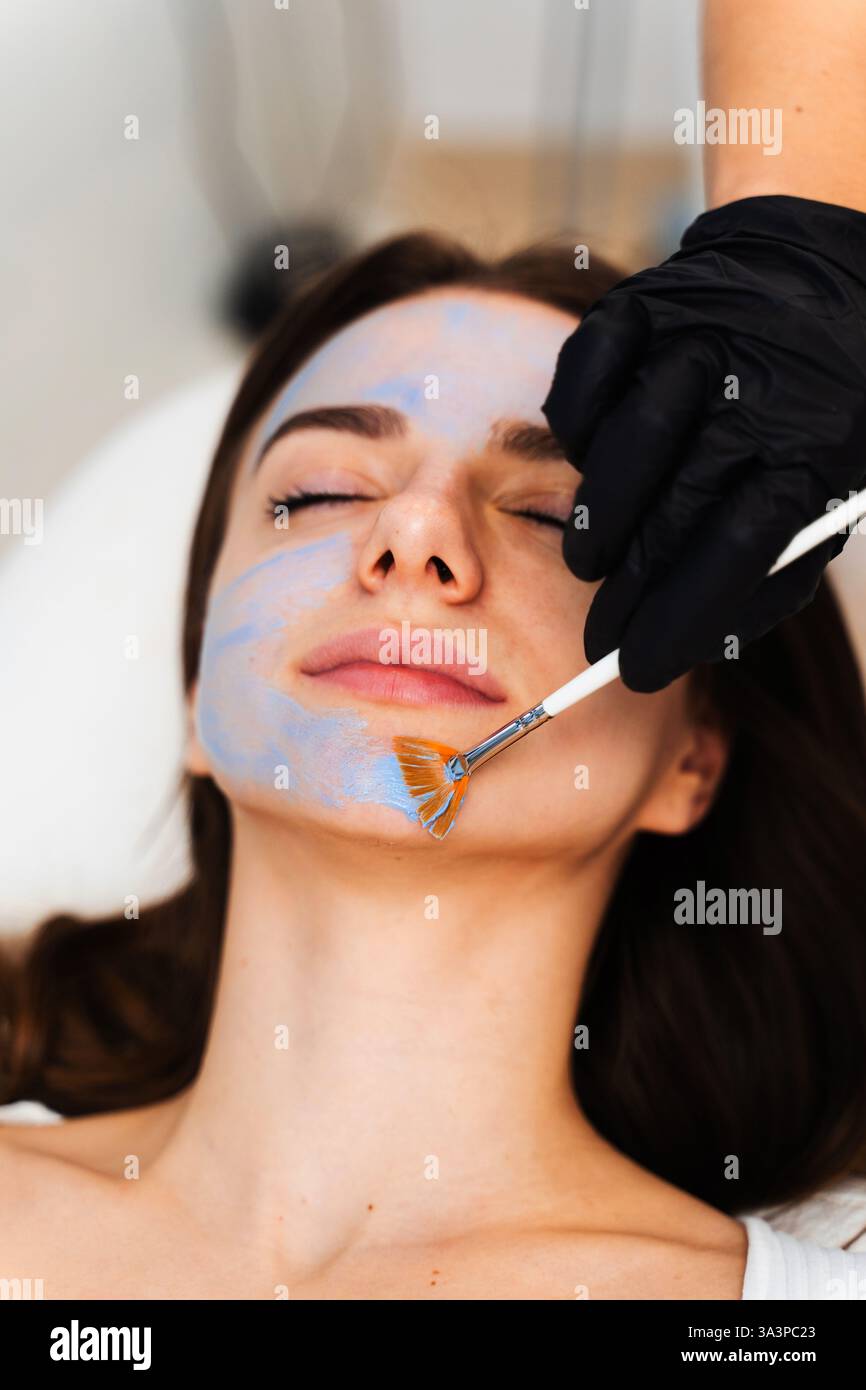 Moisturizing face skin with blue creamy mask. Caucasian young girl ...