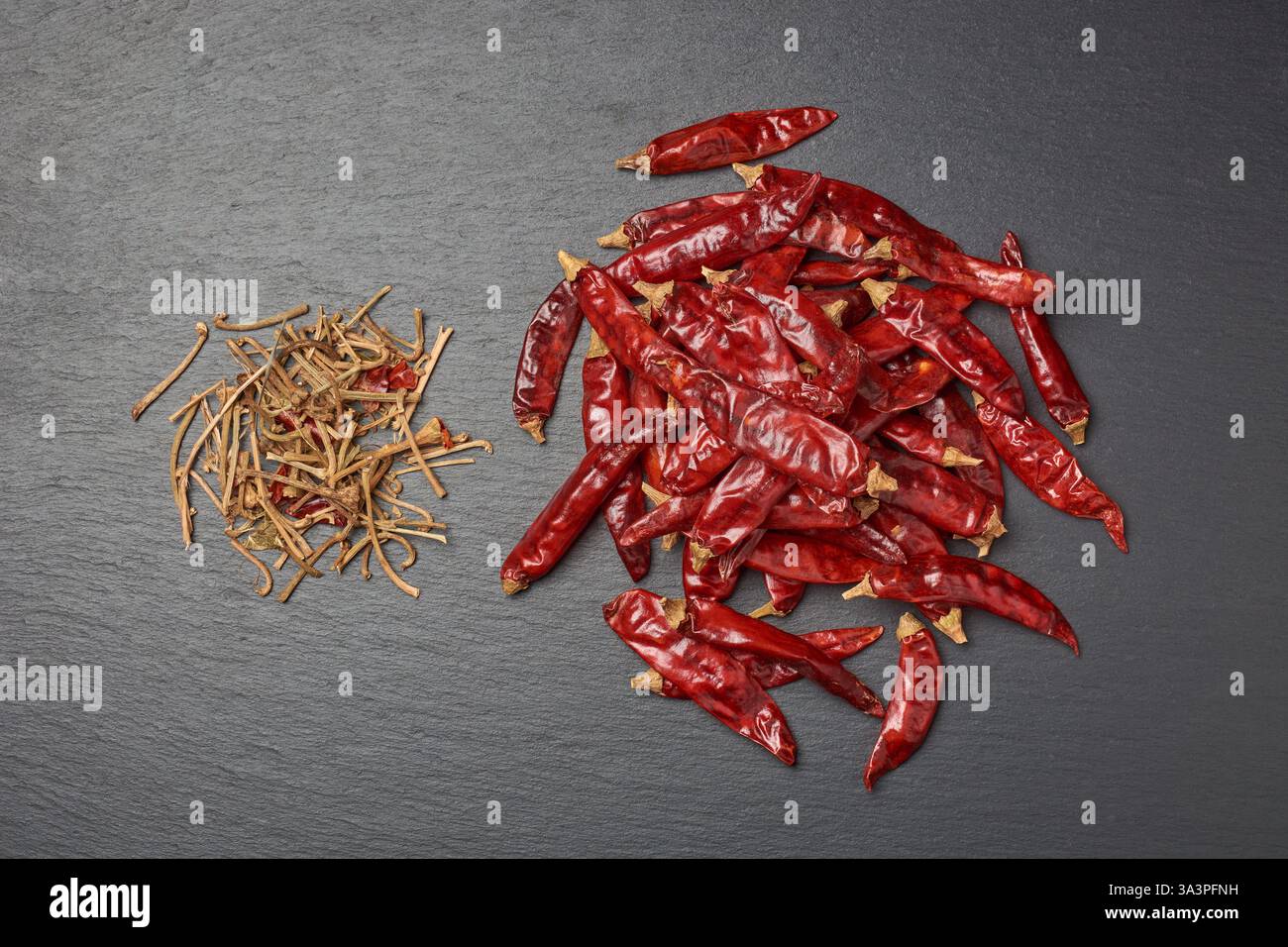 pile of dried chili peppers with stem cut off on black textured surface ...