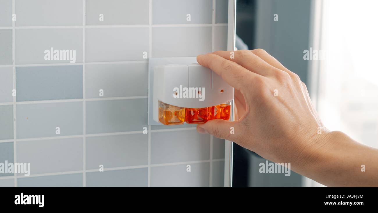 closeup of a man plugging a plug-in air freshener into a socket on a ...