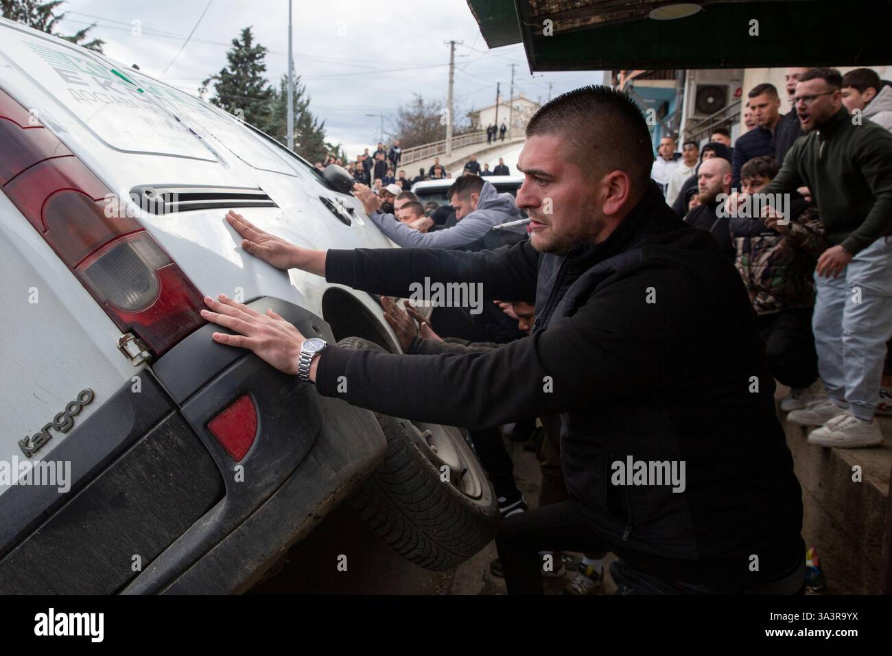 People push a car on its side while protesting near the home of the ...