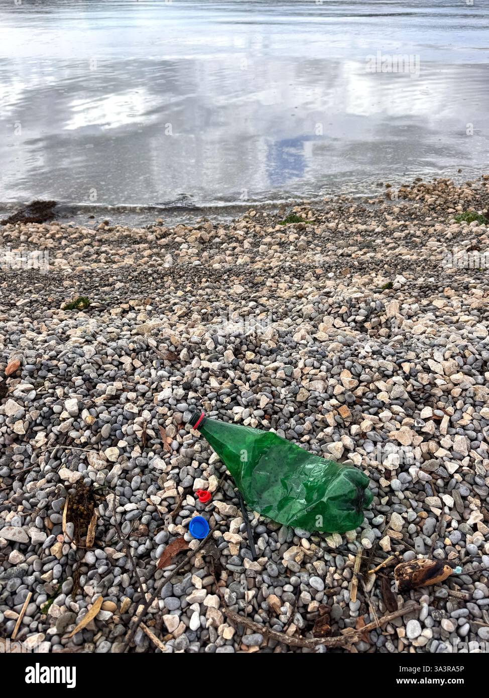 A green crumpled plastic bottle and blue cap lie on a public beach ...