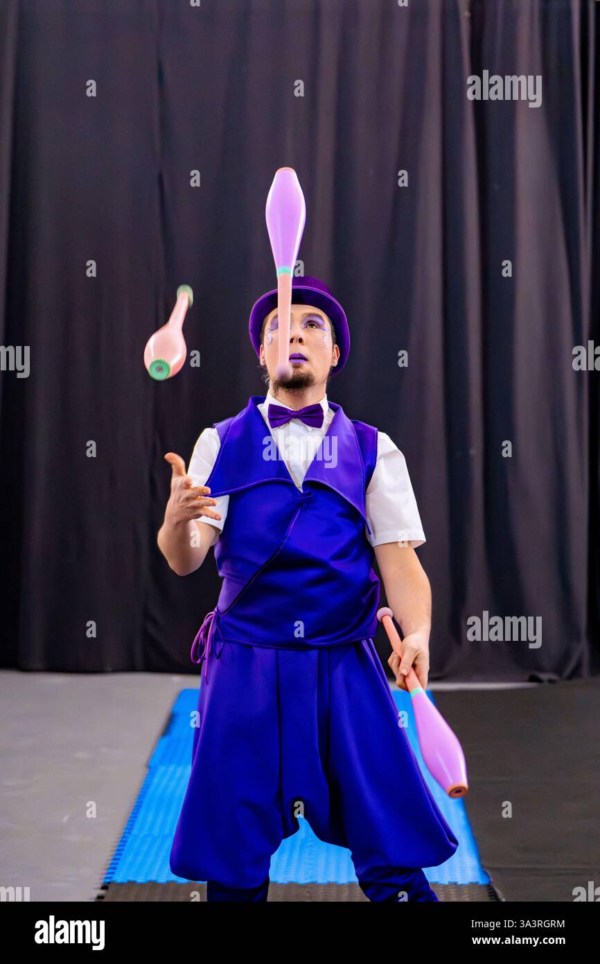Juggler in a vibrant purple costume skillfully juggles clubs on a stage ...