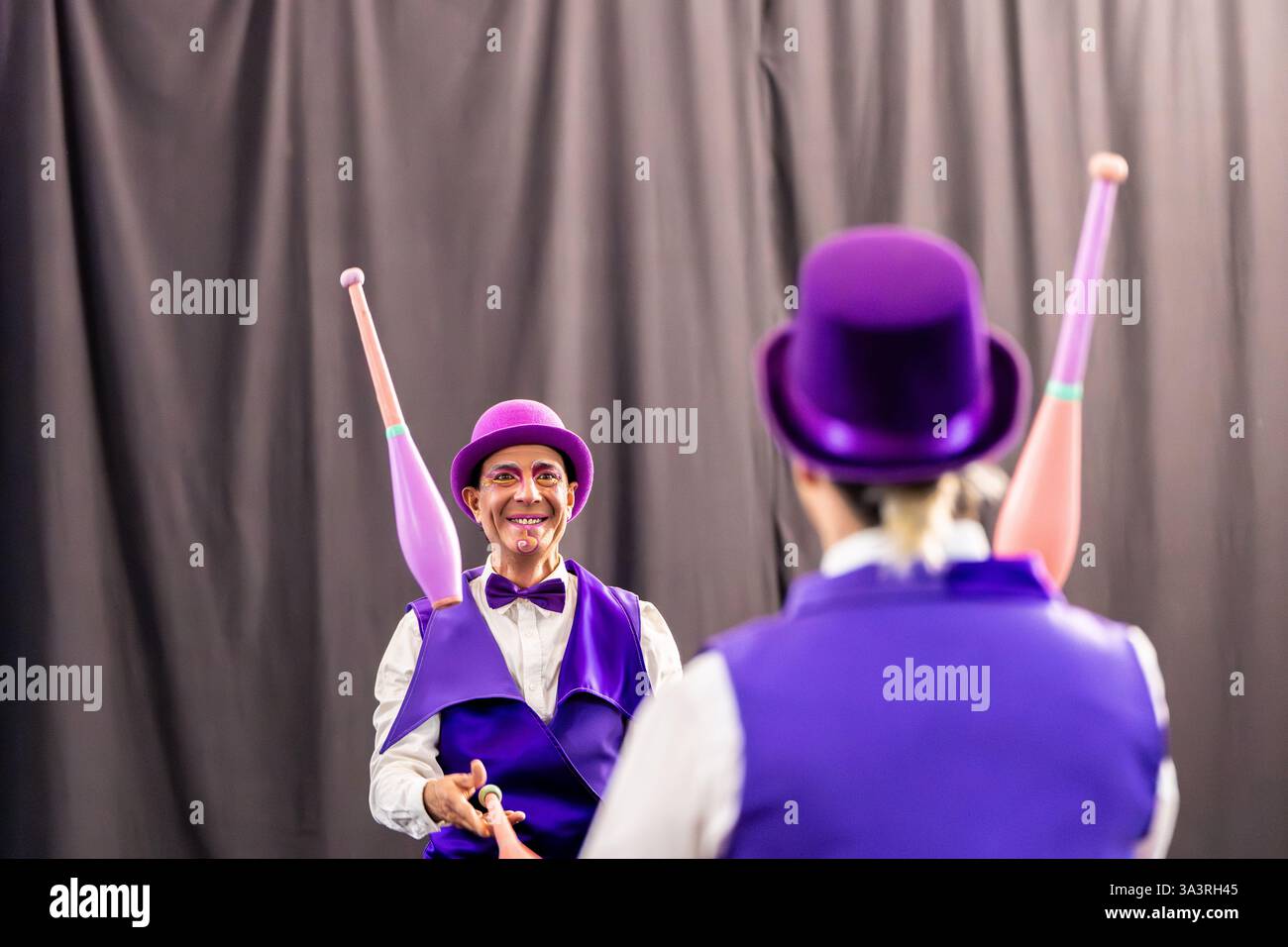 Two jugglers wearing purple costumes and bowler hats practicing their ...