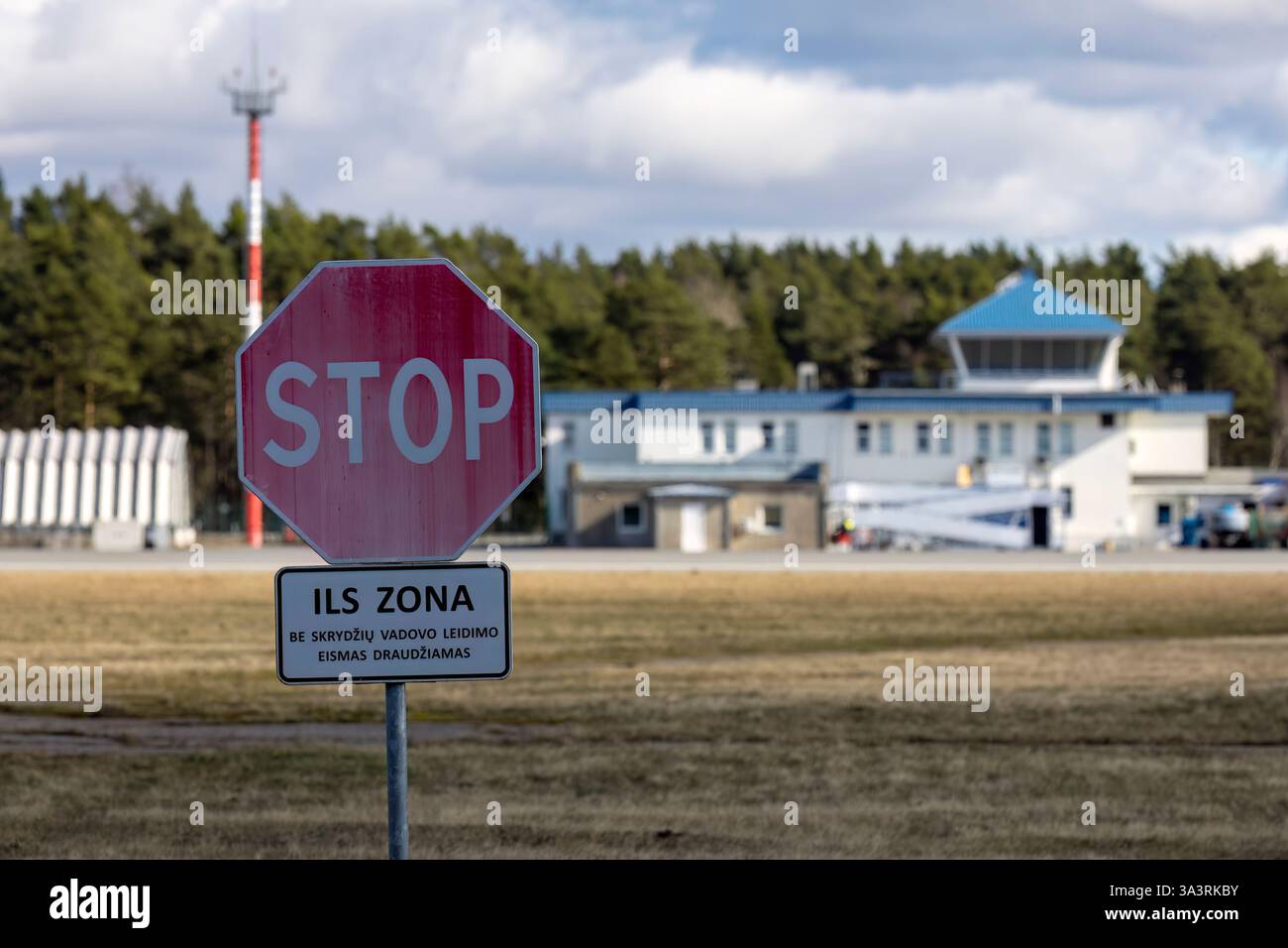 A stop sign with an "ILS Zona" warning in Lithuanian stands in an ...