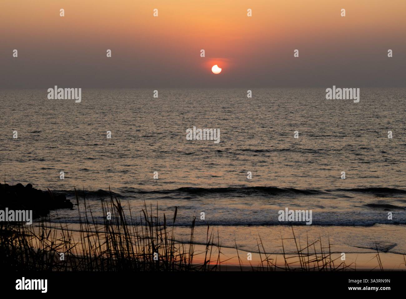 A mesmerizing Solar Eclipse-sunset over the vast ocean, with gentle waves rolling onto the shore ...