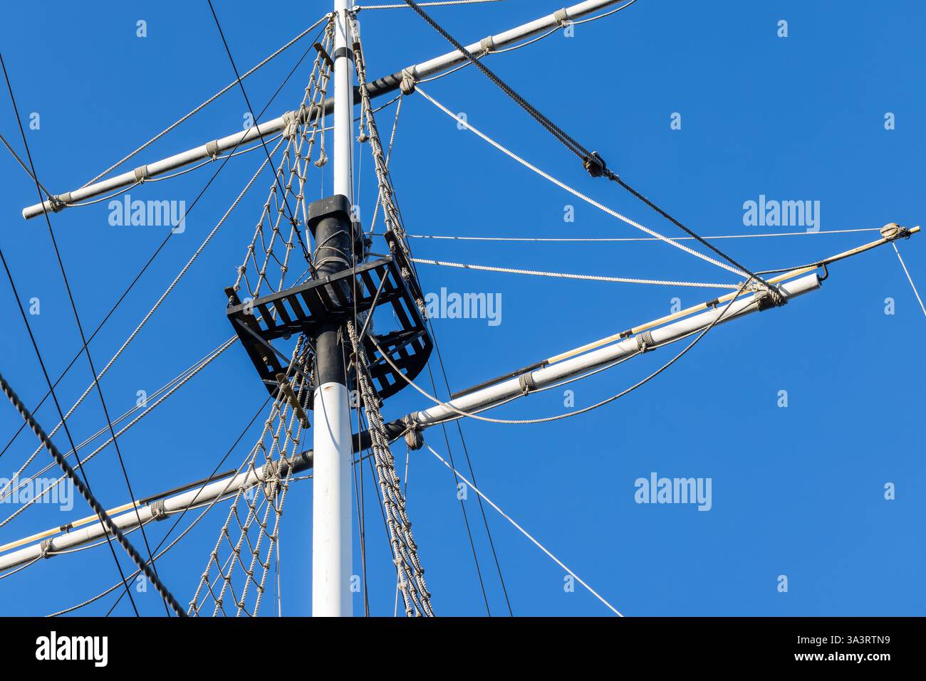 White ships mast, black platform, and rigged ropes are under blue sky ...