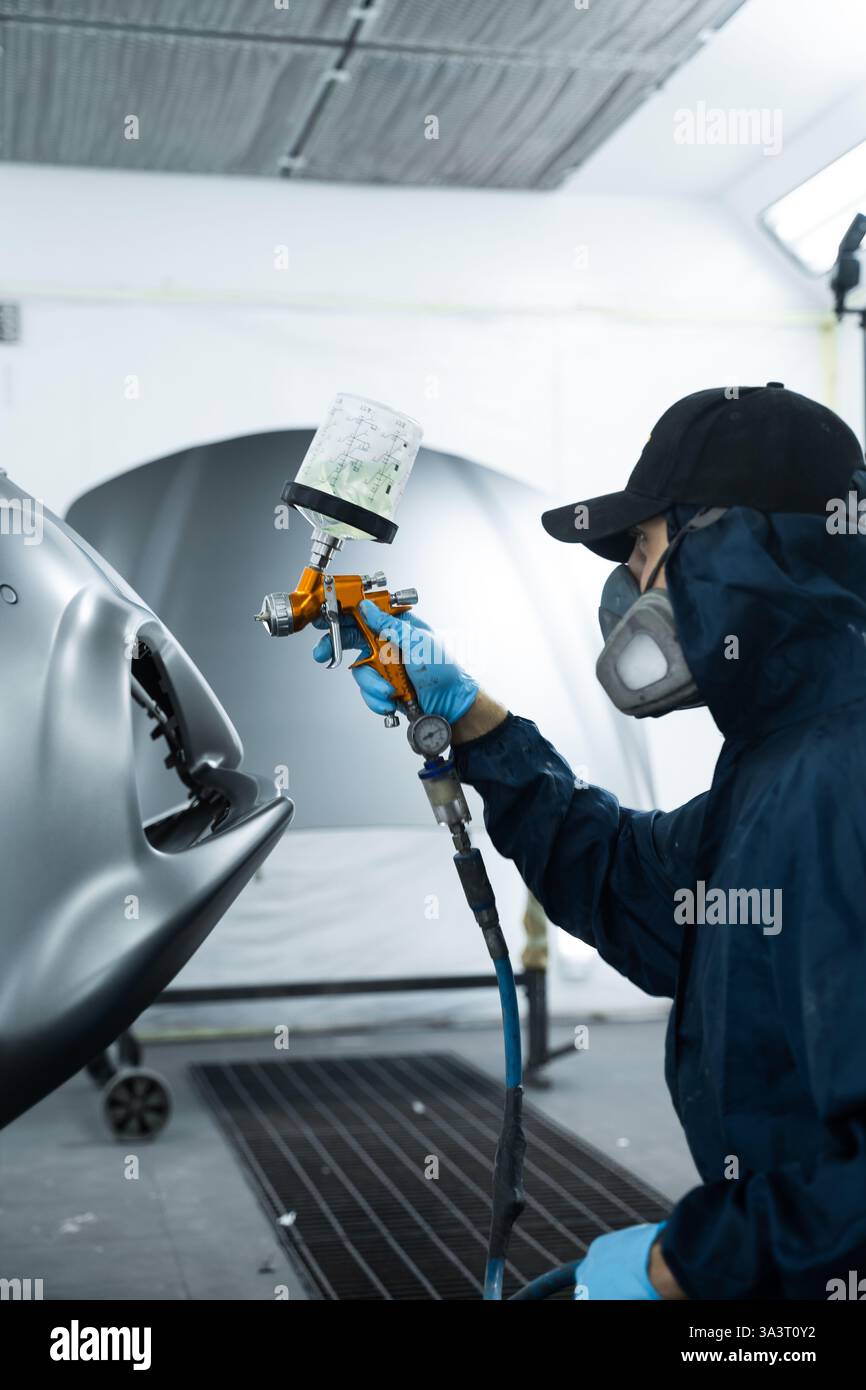 Car painter is applying lacquer on car using LVLP spray gun. Putting ...
