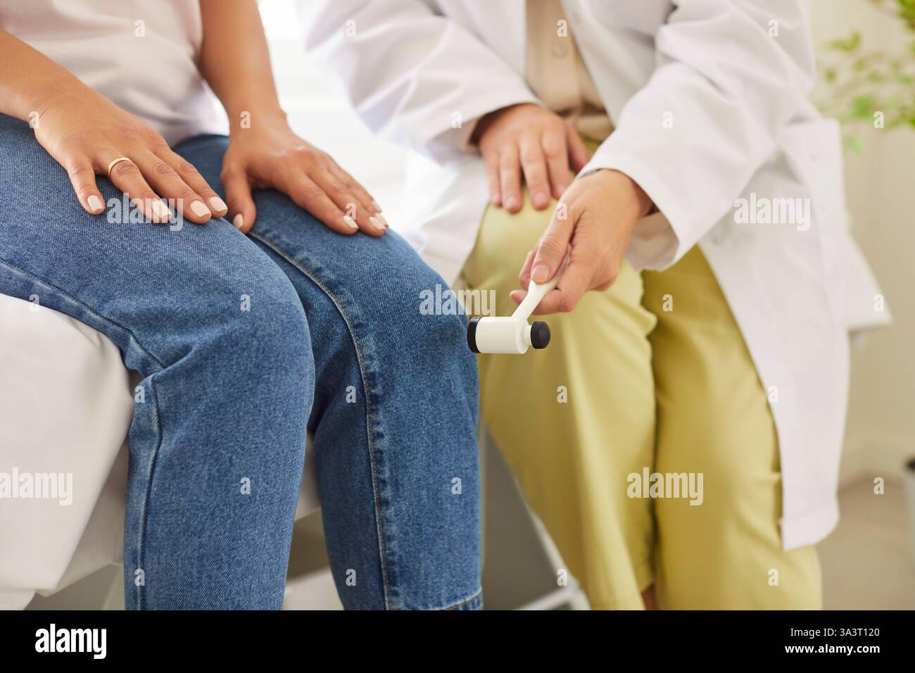 Neurologist testing female patient knee reflex with hammer during ...