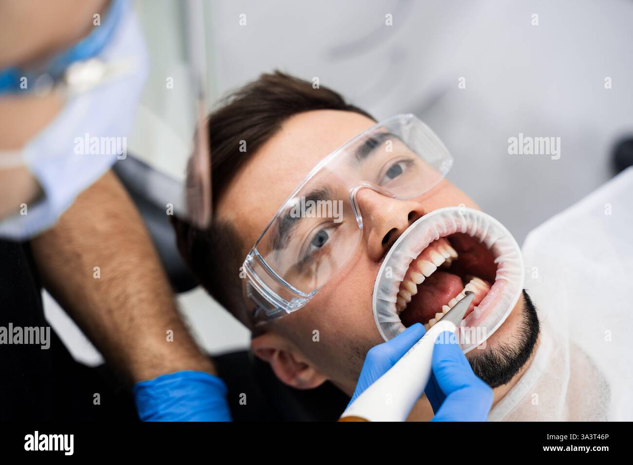 Airflow teeth cleaning process. Dentist removes plaque from teeth with ...