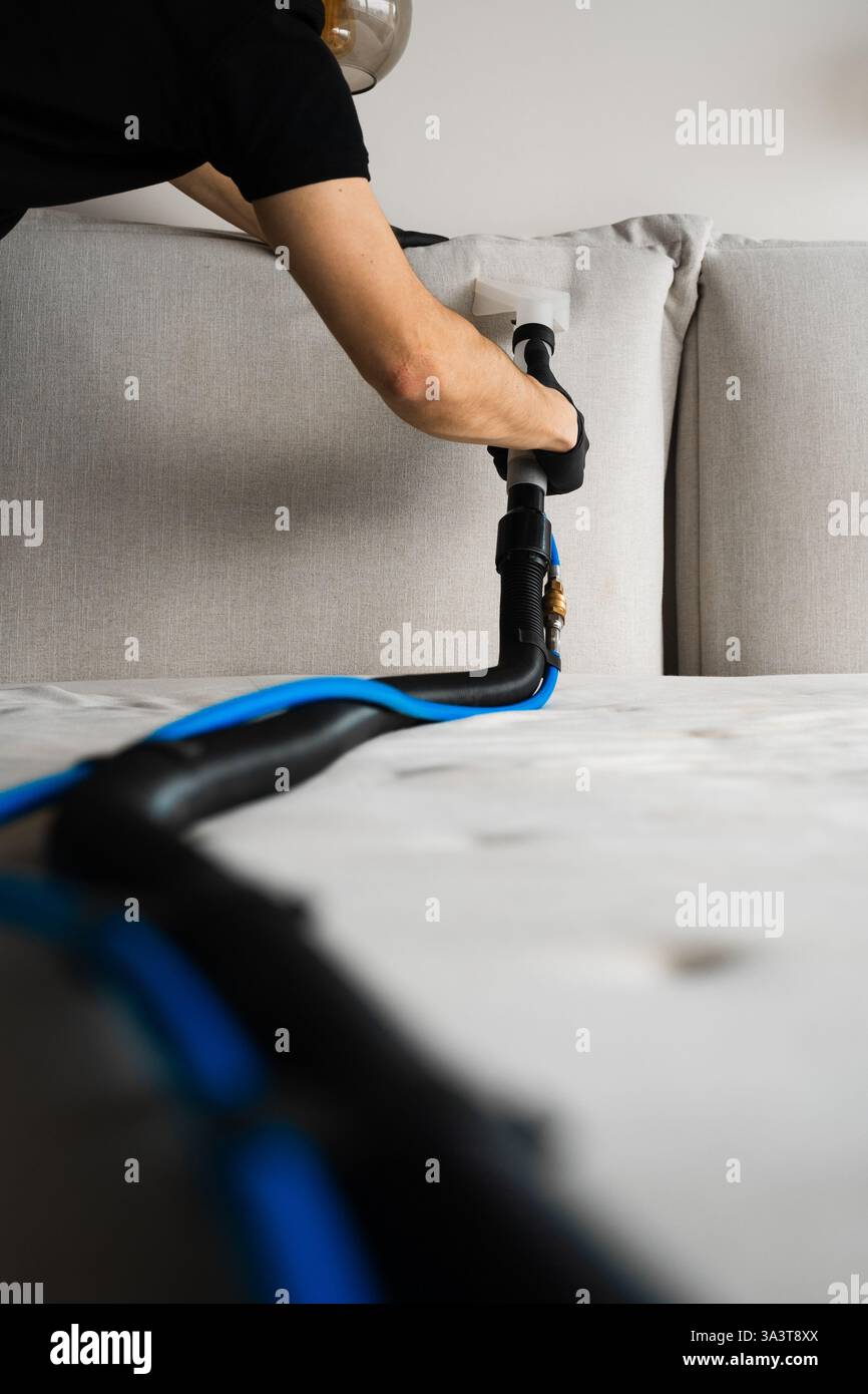 Cleaner is washing off couch from stains, dust and dirt using extractor ...