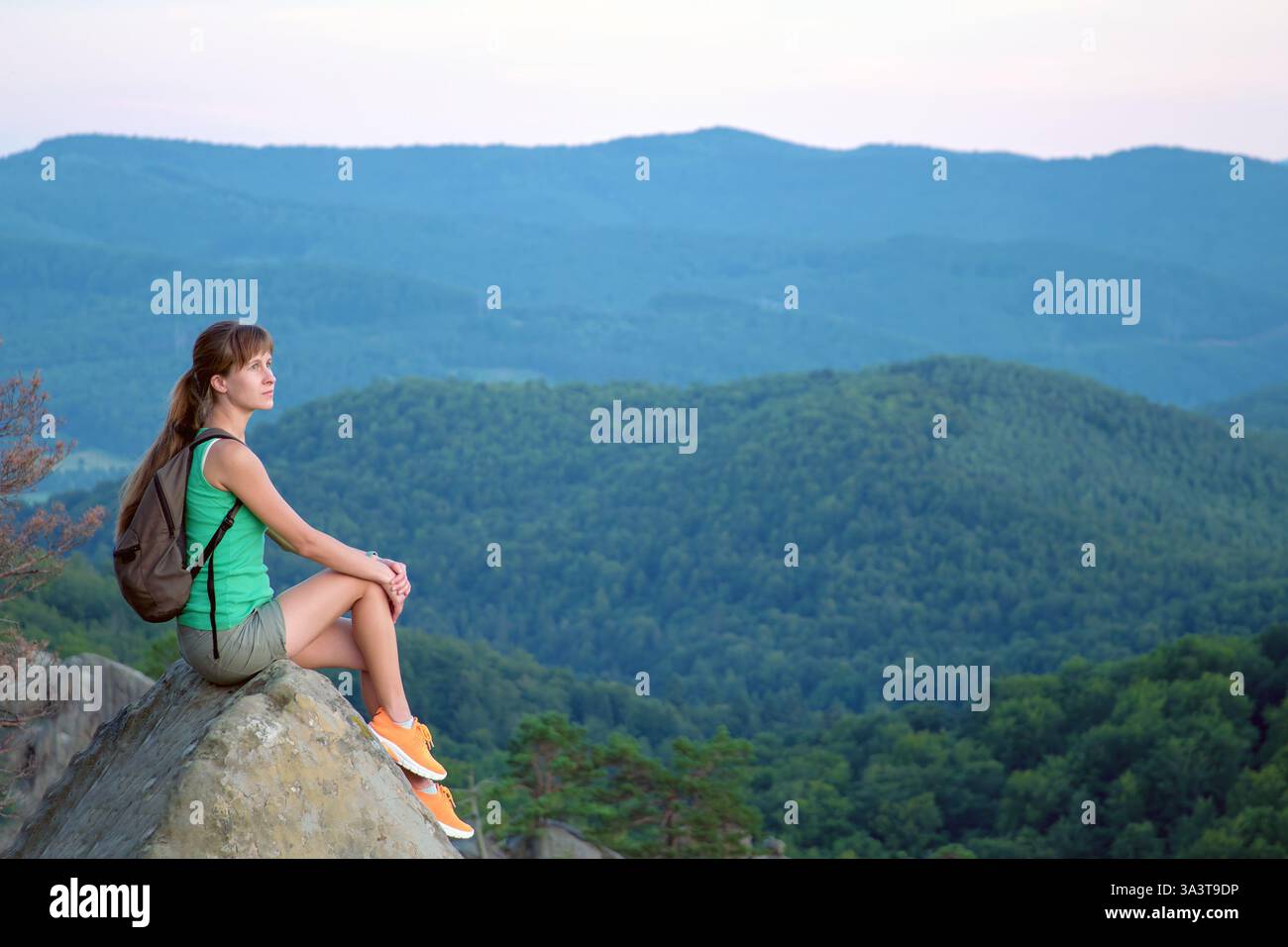 Sportive woman sitting alone taking a break on hillside trail. Female hiker enjoying view of ...