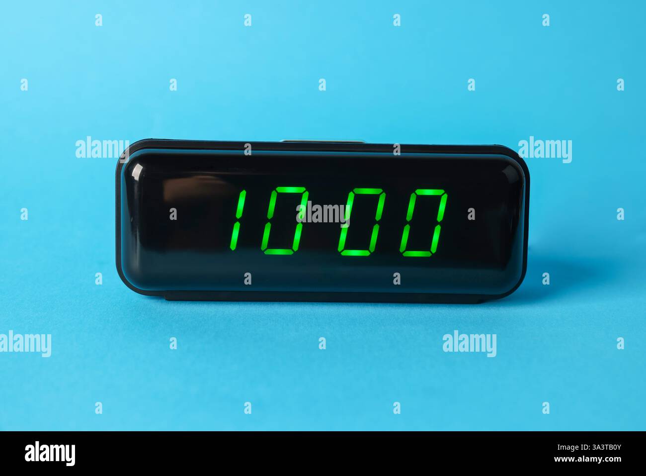 Digital alarm clock showing 10:00 o'clock on light blue background ...
