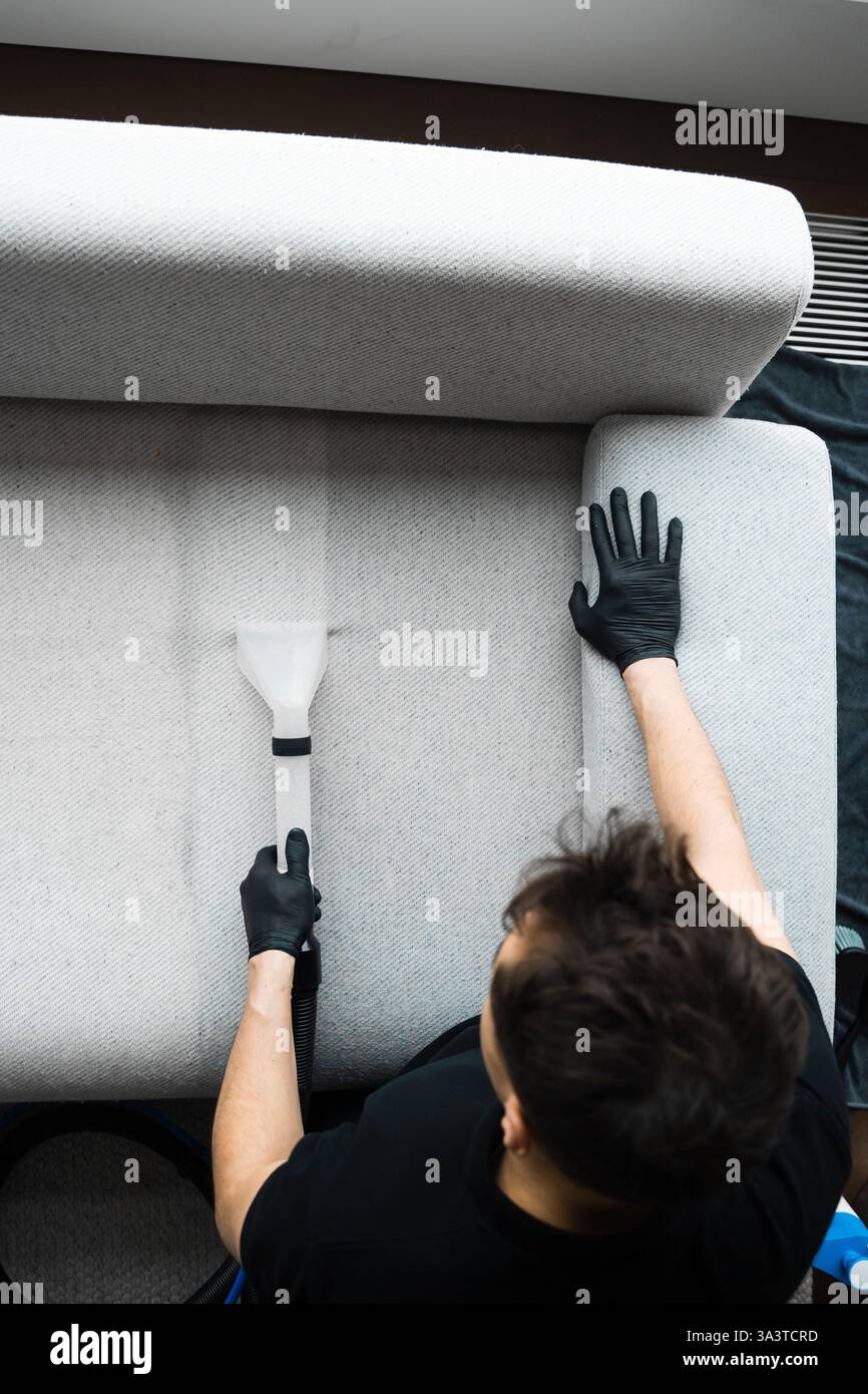 Cleaner is dry-cleaning sofa using extractor machine with detergent ...